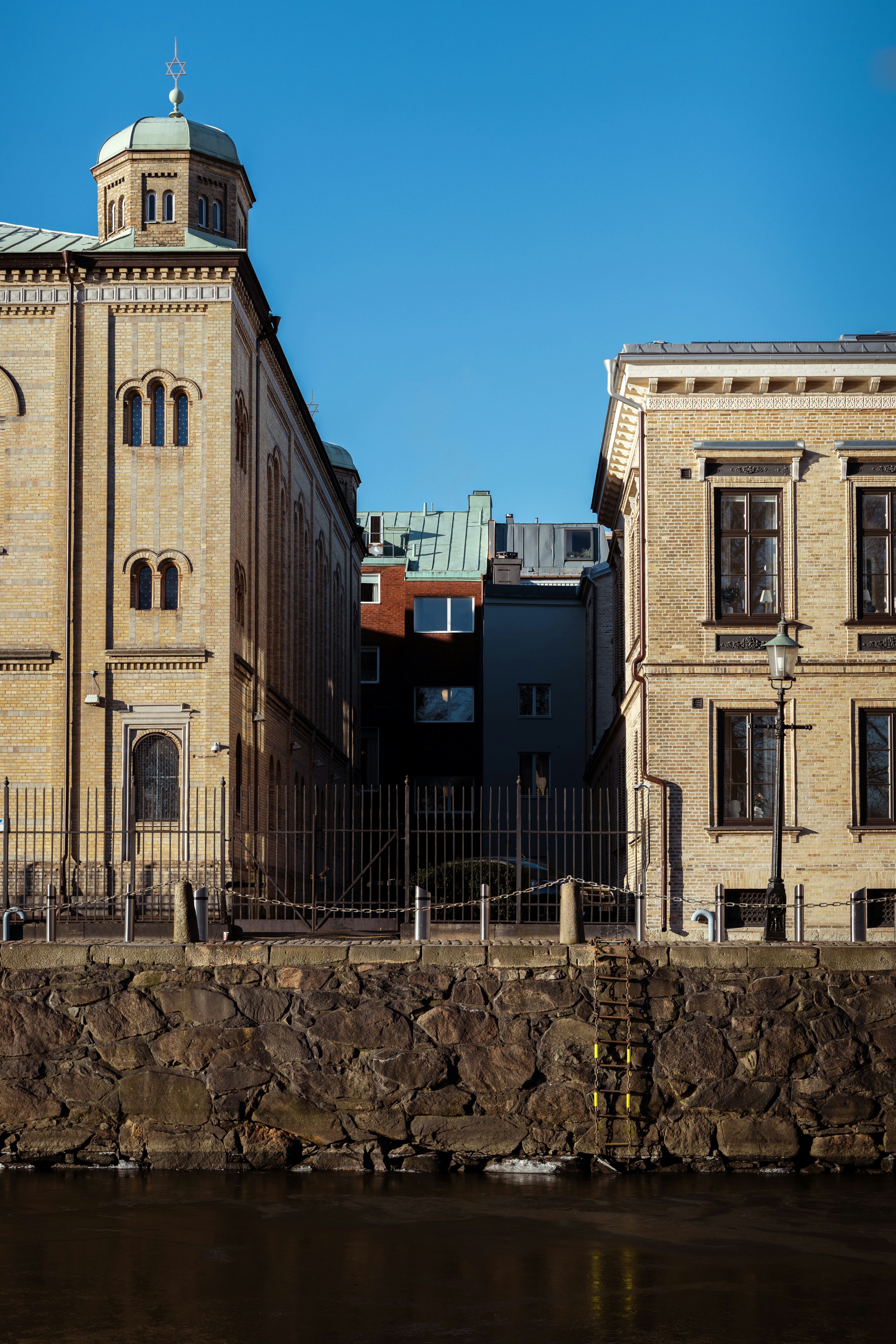 Between Brick Giants: A Narrow Riverside Gap Under Blue Sky