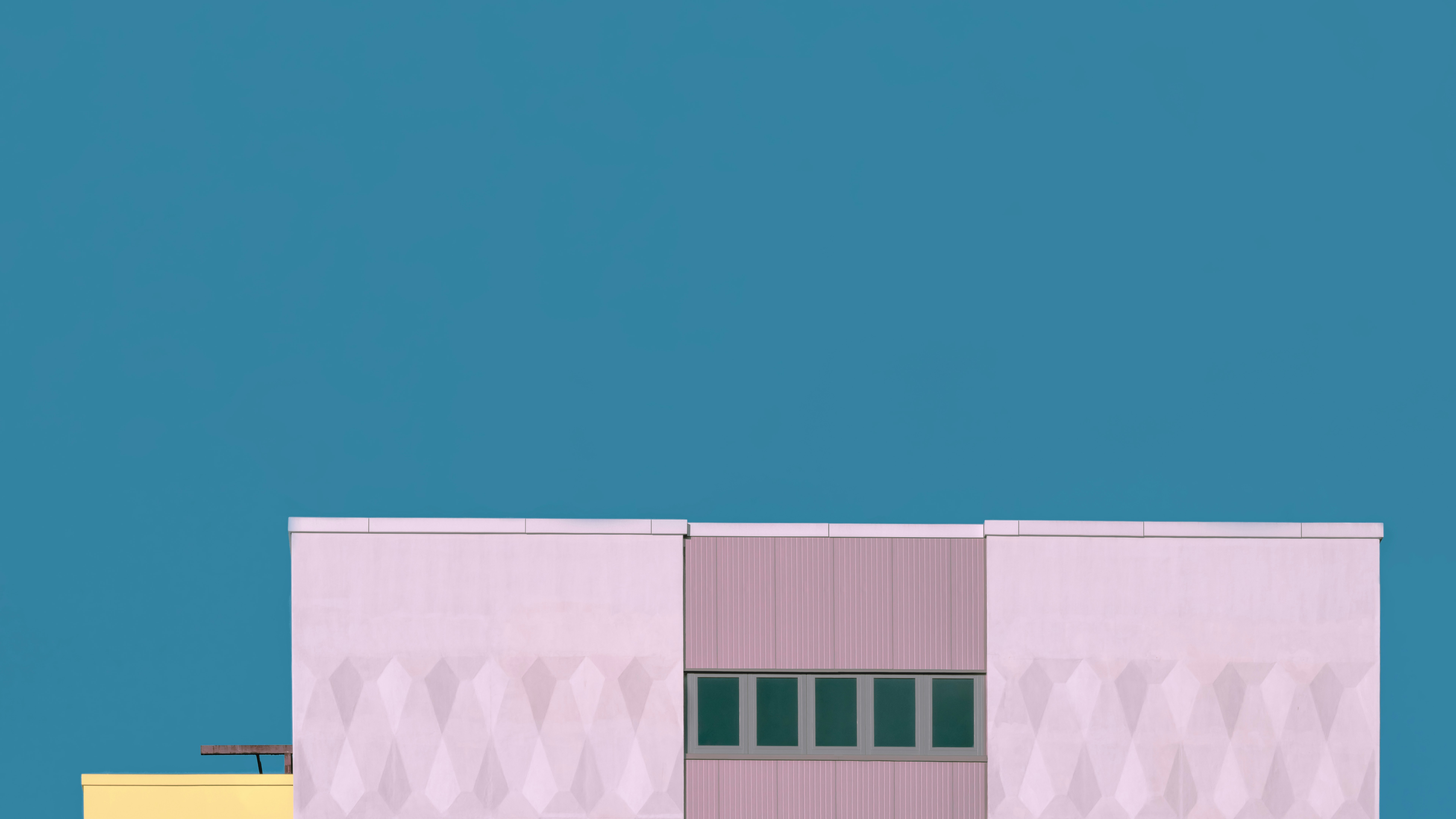 Minimalist architecture with pastel hues under a vibrant teal sky.