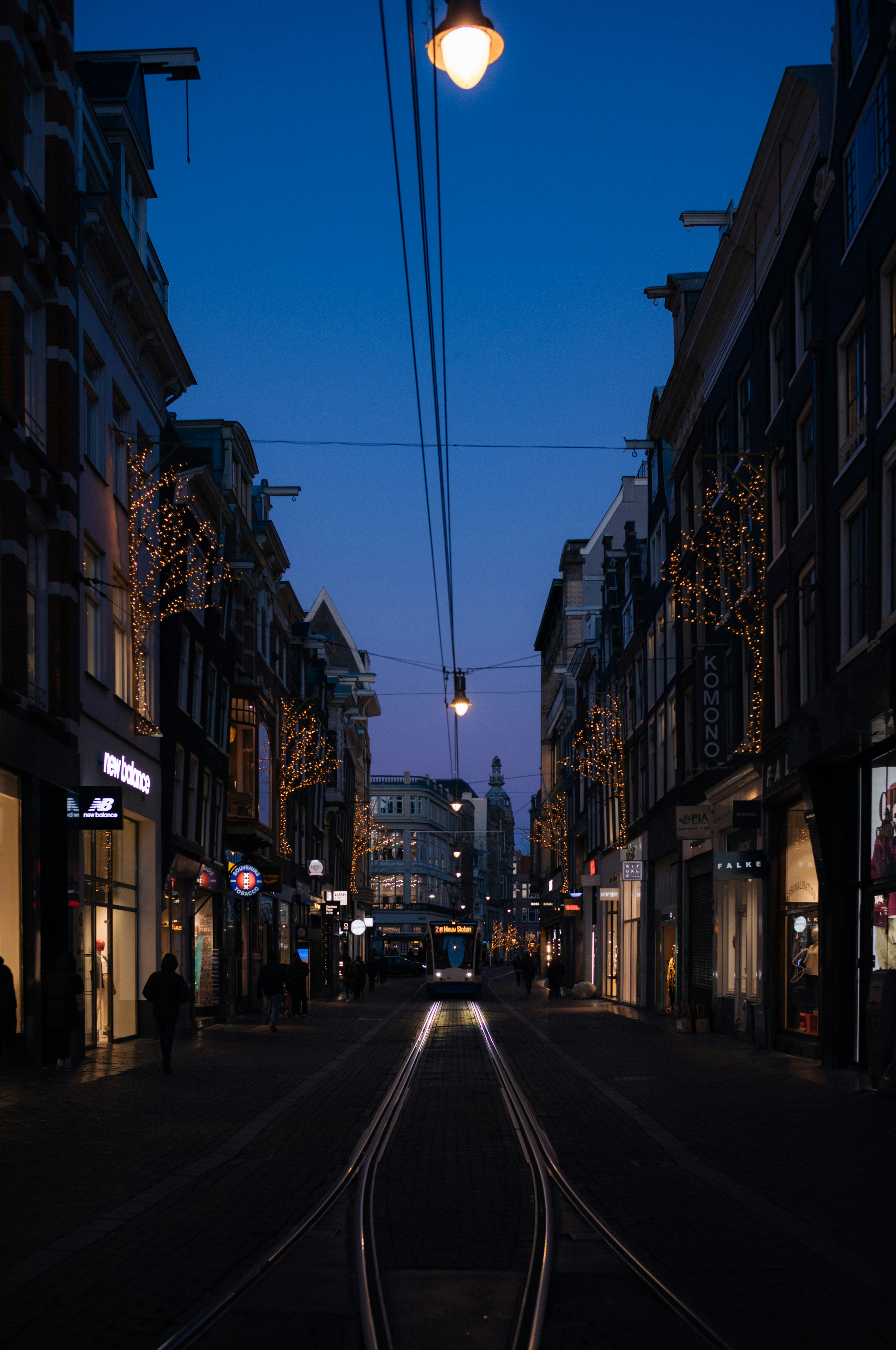 Twilight street scene with tram tracks leading through a decorated urban area, adorned with festive lights under a deep blue sky.