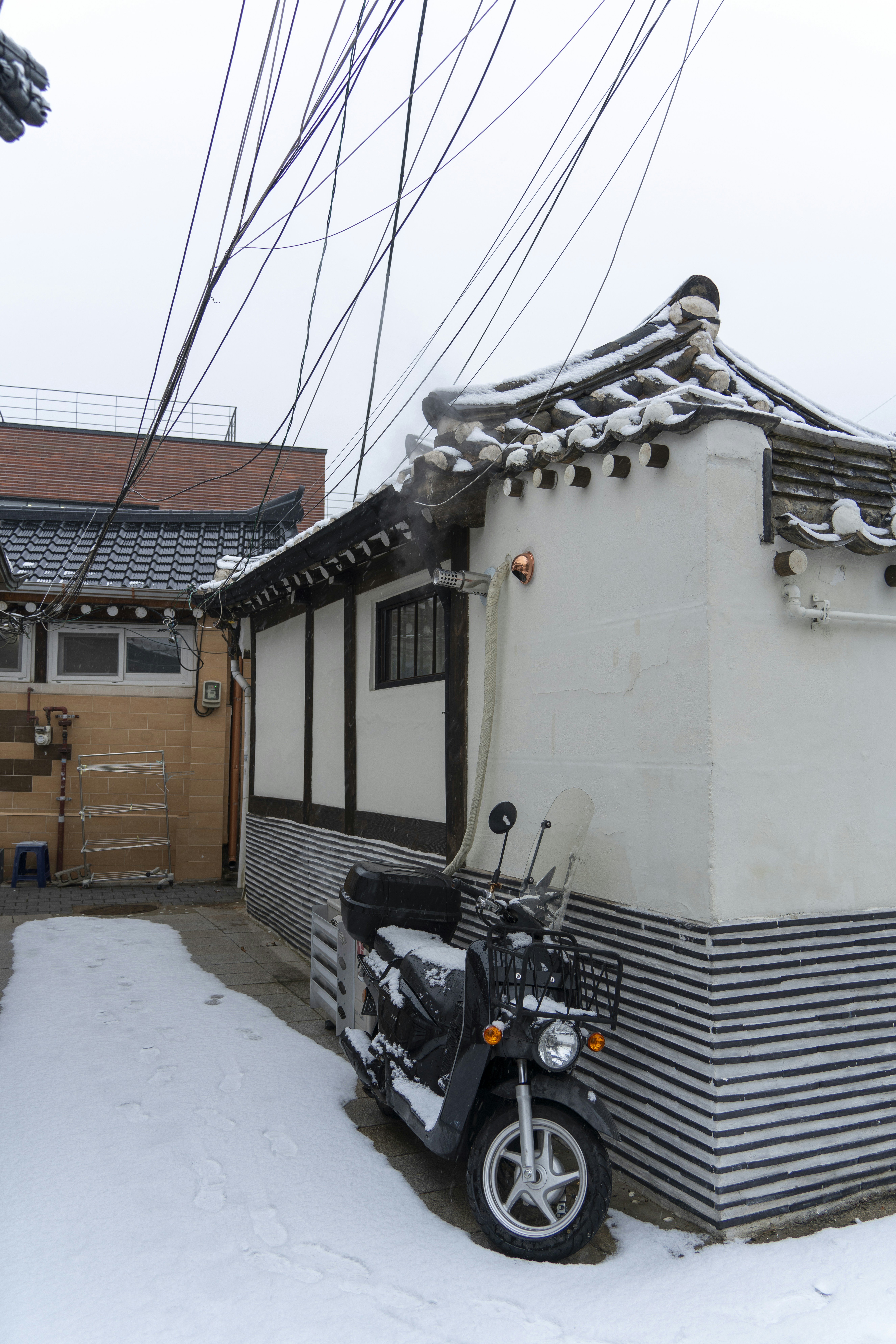 Snowbound Courtyard: A Retro Scooter Nestled by a White-Walled Hanok Under a Web of Wires