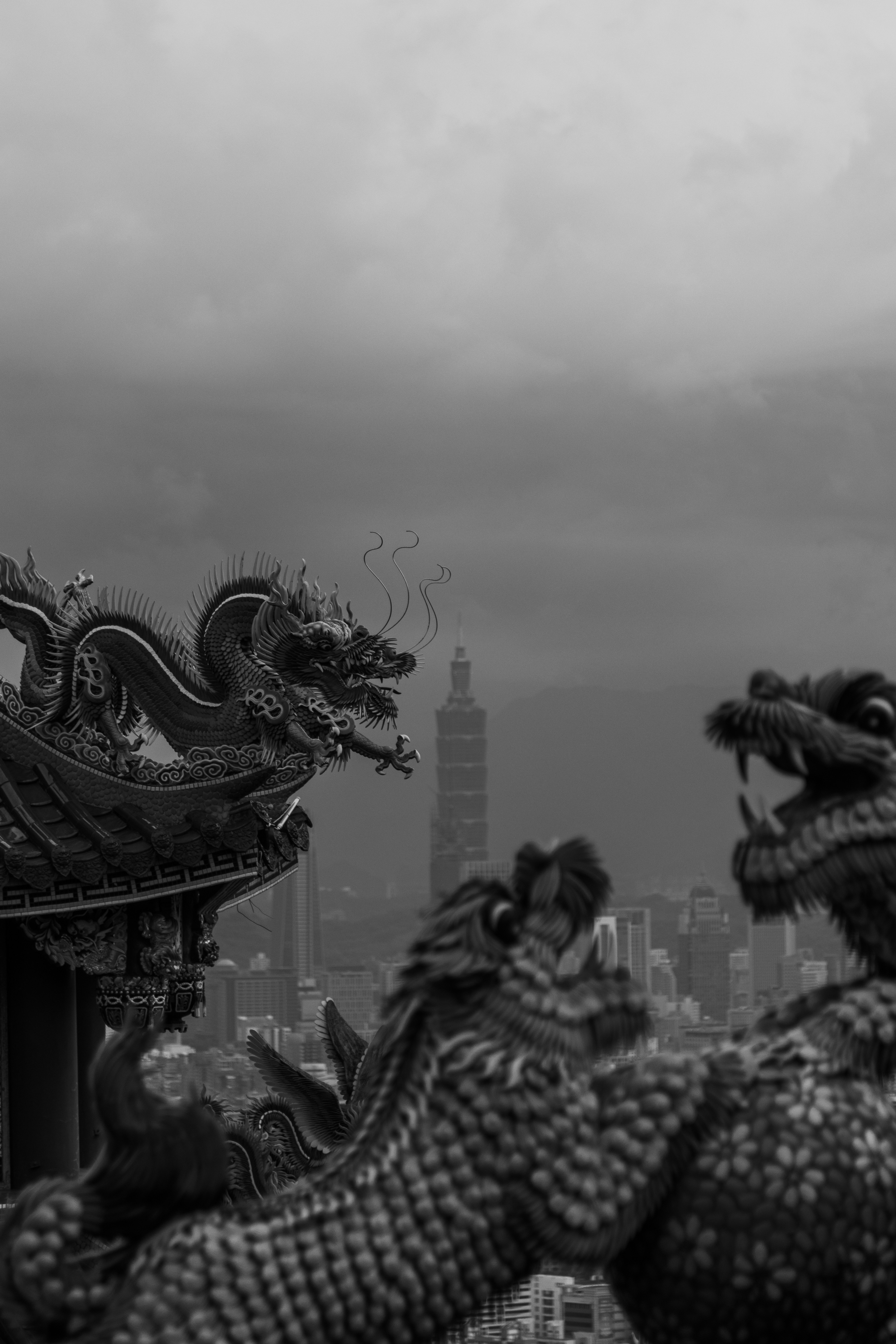 Intricate dragon sculptures overlook the Taipei skyline, featuring the iconic Taipei 101 in the background against a dramatic sky.