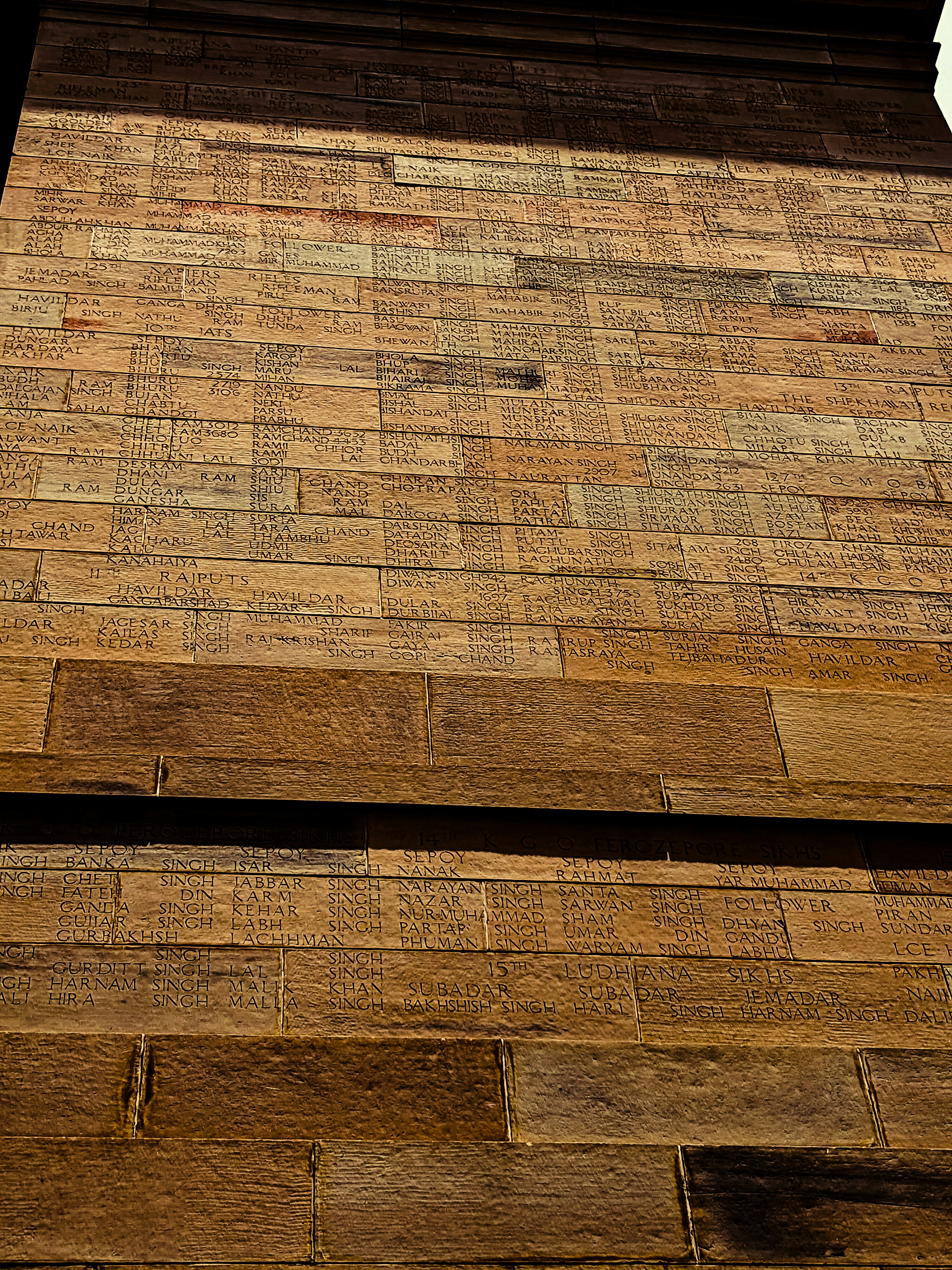 Warm sandstone bricks form a repetitive facade with pronounced mortar lines. A dark shadow bands the top portion, emphasizing texture and depth.