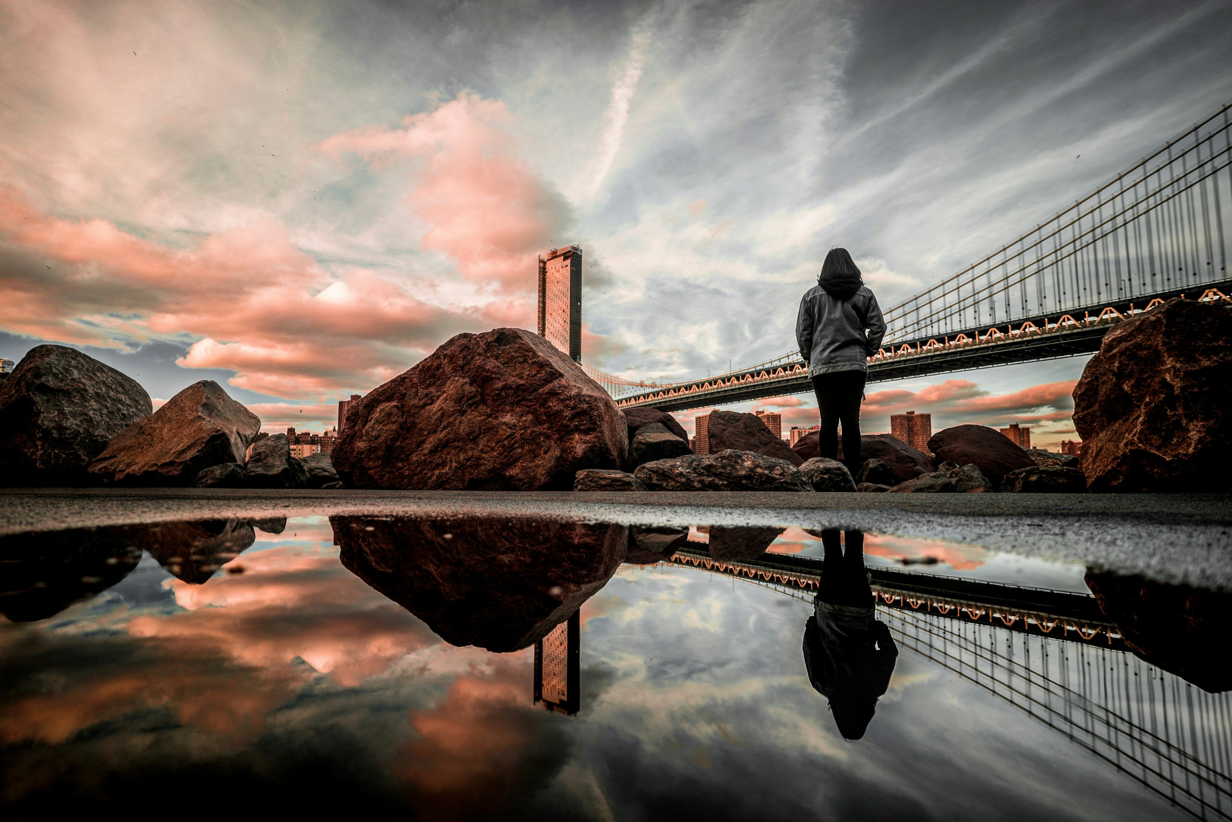 Reflection at the Tidal Edge: A figure on the rocks beneath a high suspension span