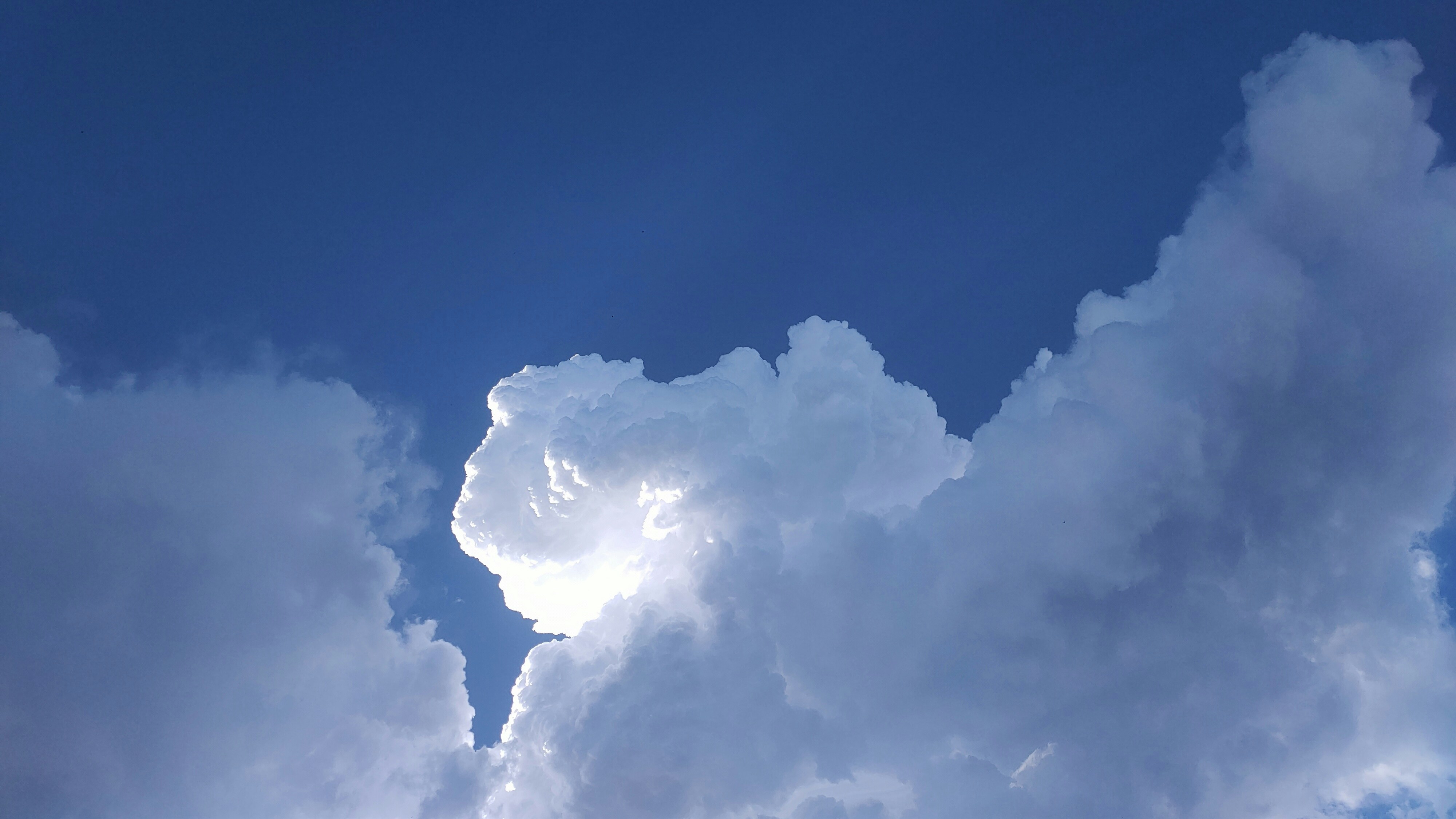 Fluffy white clouds illuminated by sunlight against a deep blue sky.