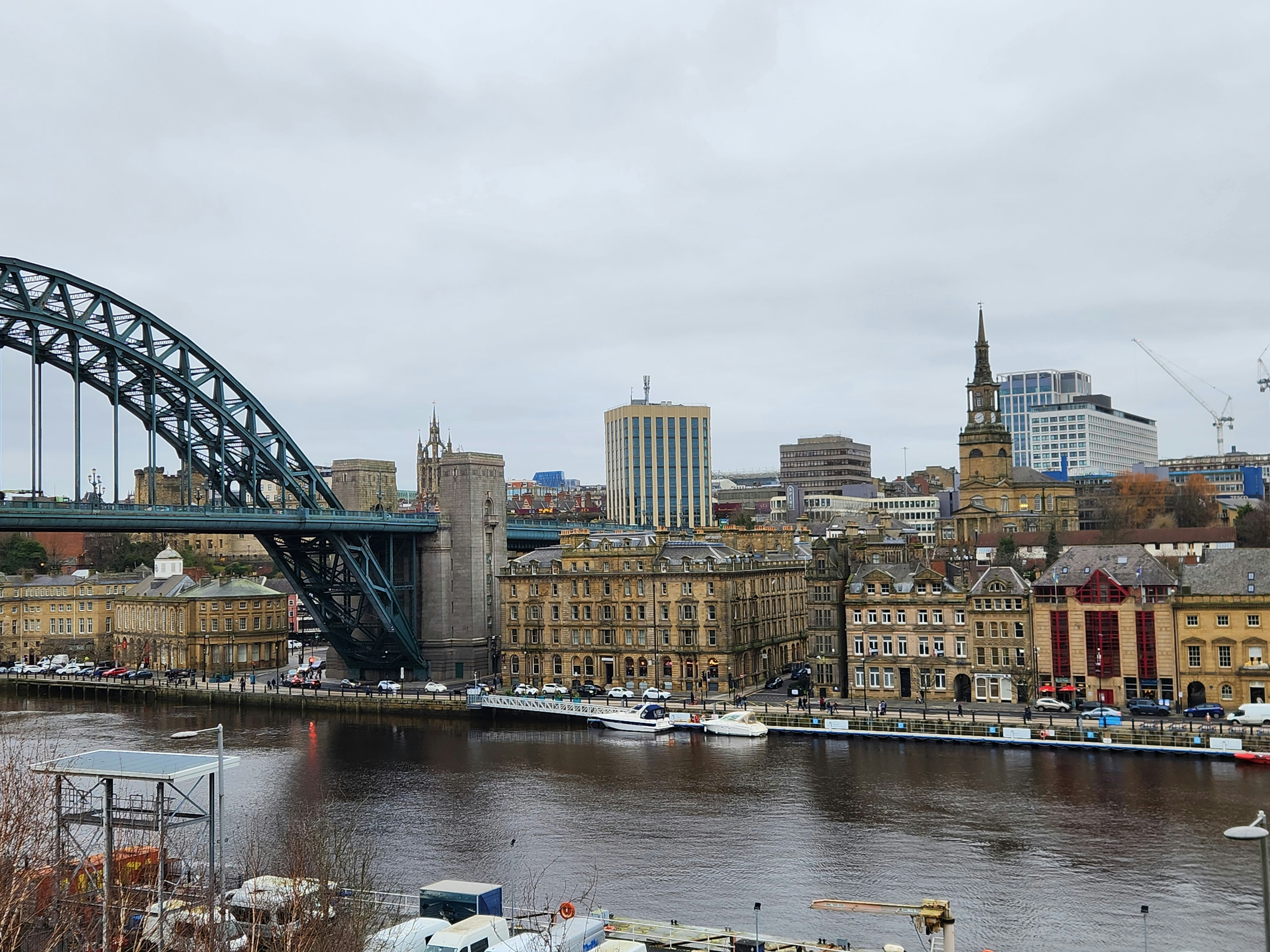Arched steel bridge spanning a river with a historic cityscape in the background.