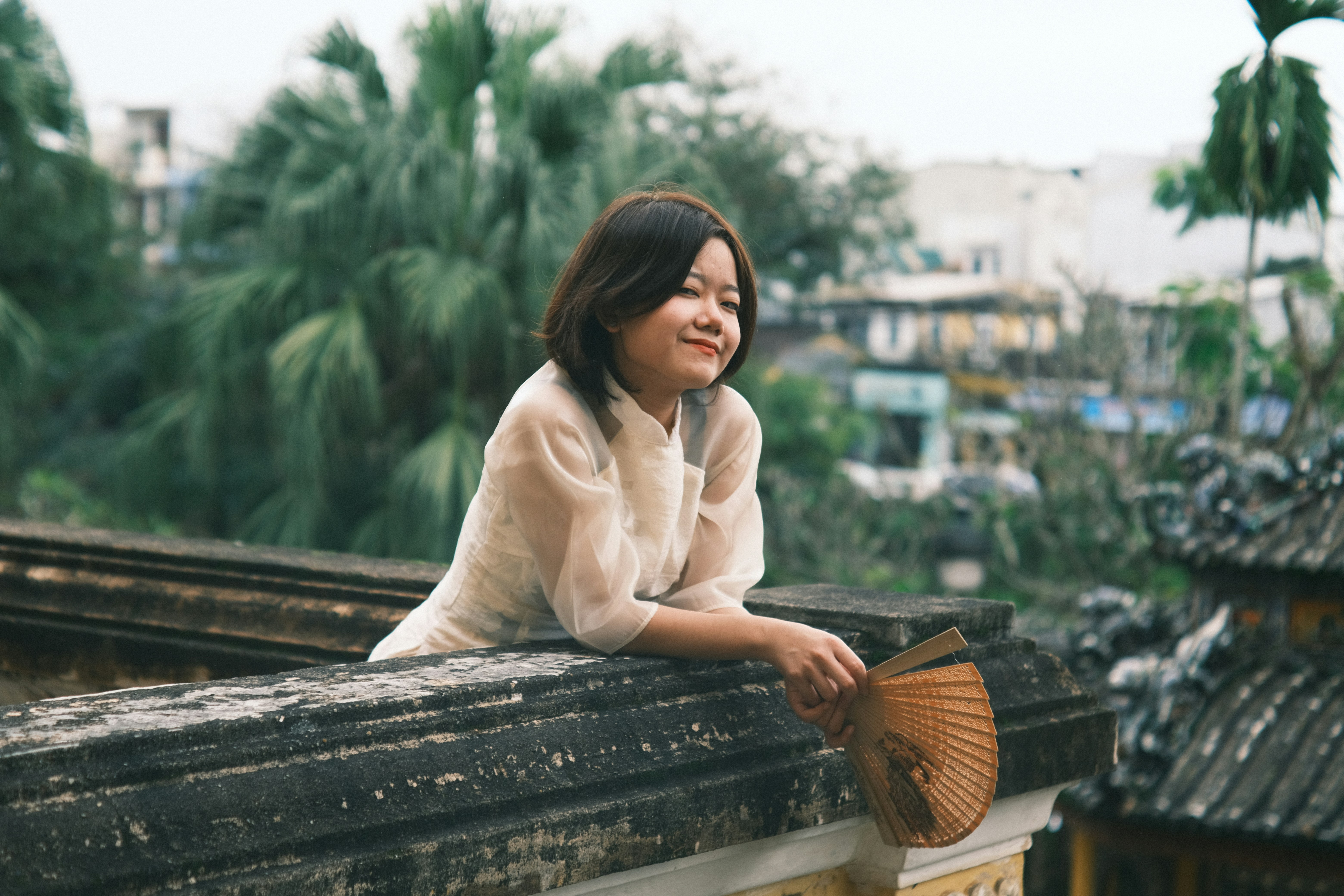 A woman sitting on a ledge holding a fan photo – Free Woman Image on ...