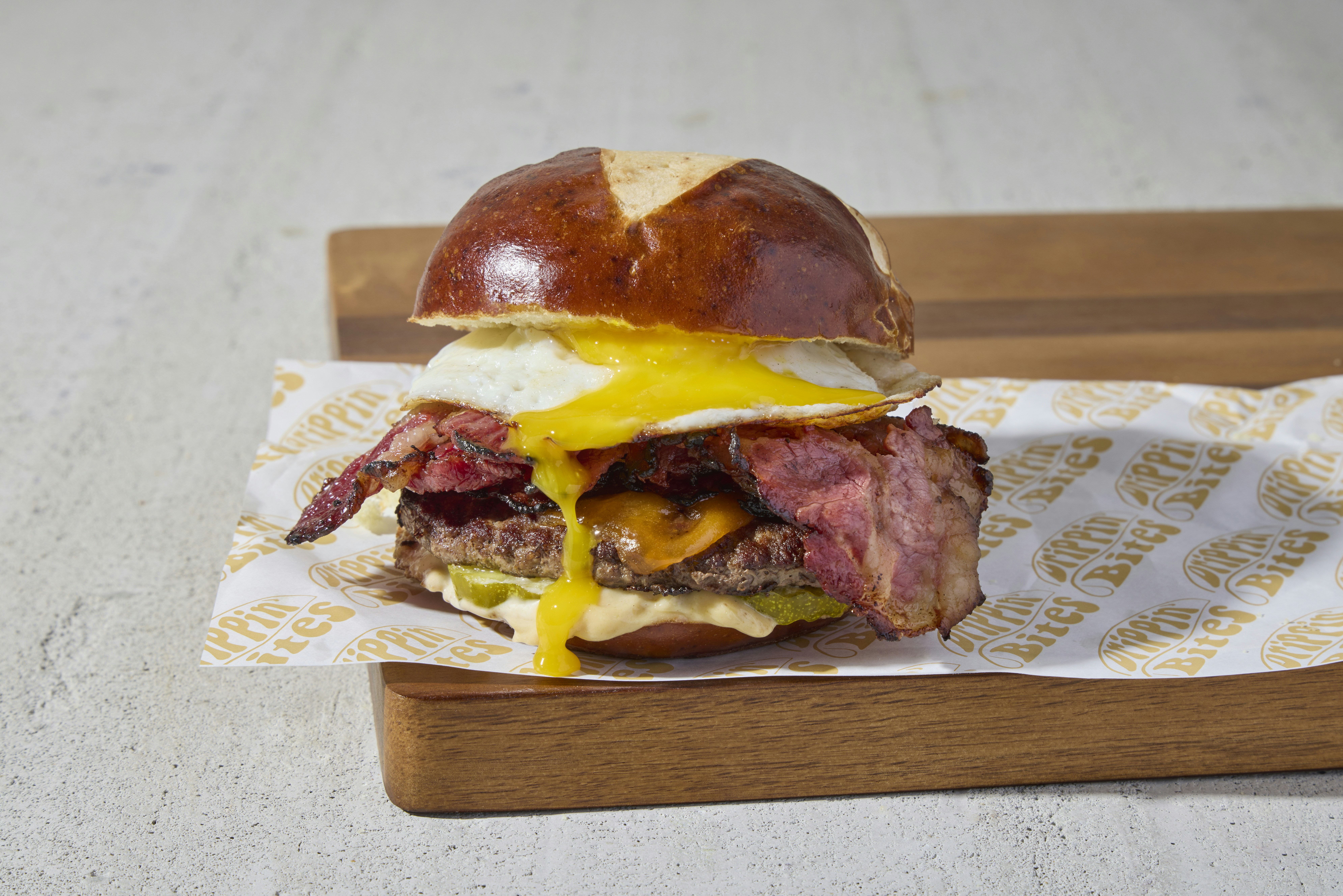 A mouthwatering burger featuring a perfectly cooked egg, crispy bacon, and melted cheese, served on a soft pretzel bun. Ideal for breakfast lovers.