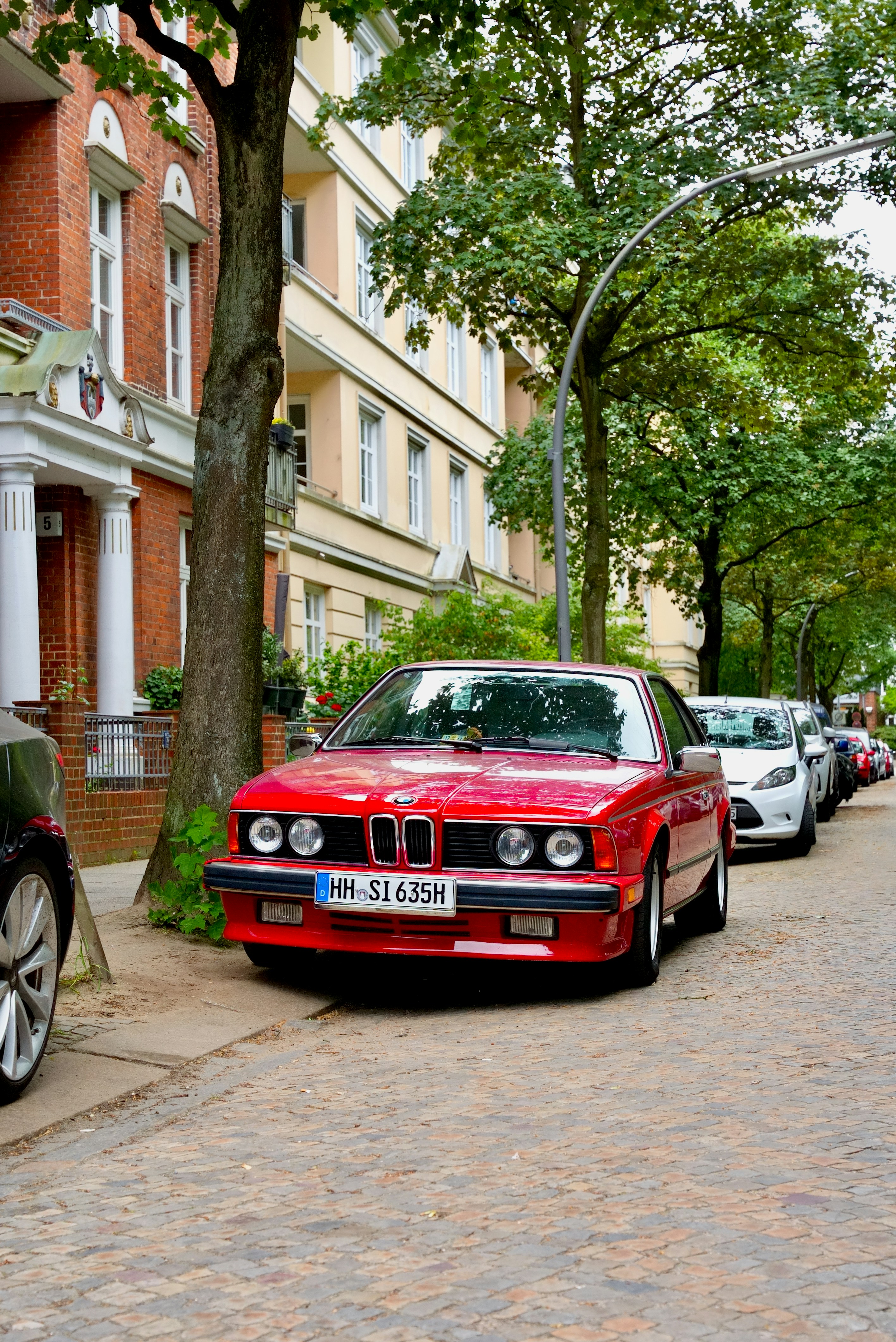 Red BMW on a Cobblestone Street Framed by Urban Trees
