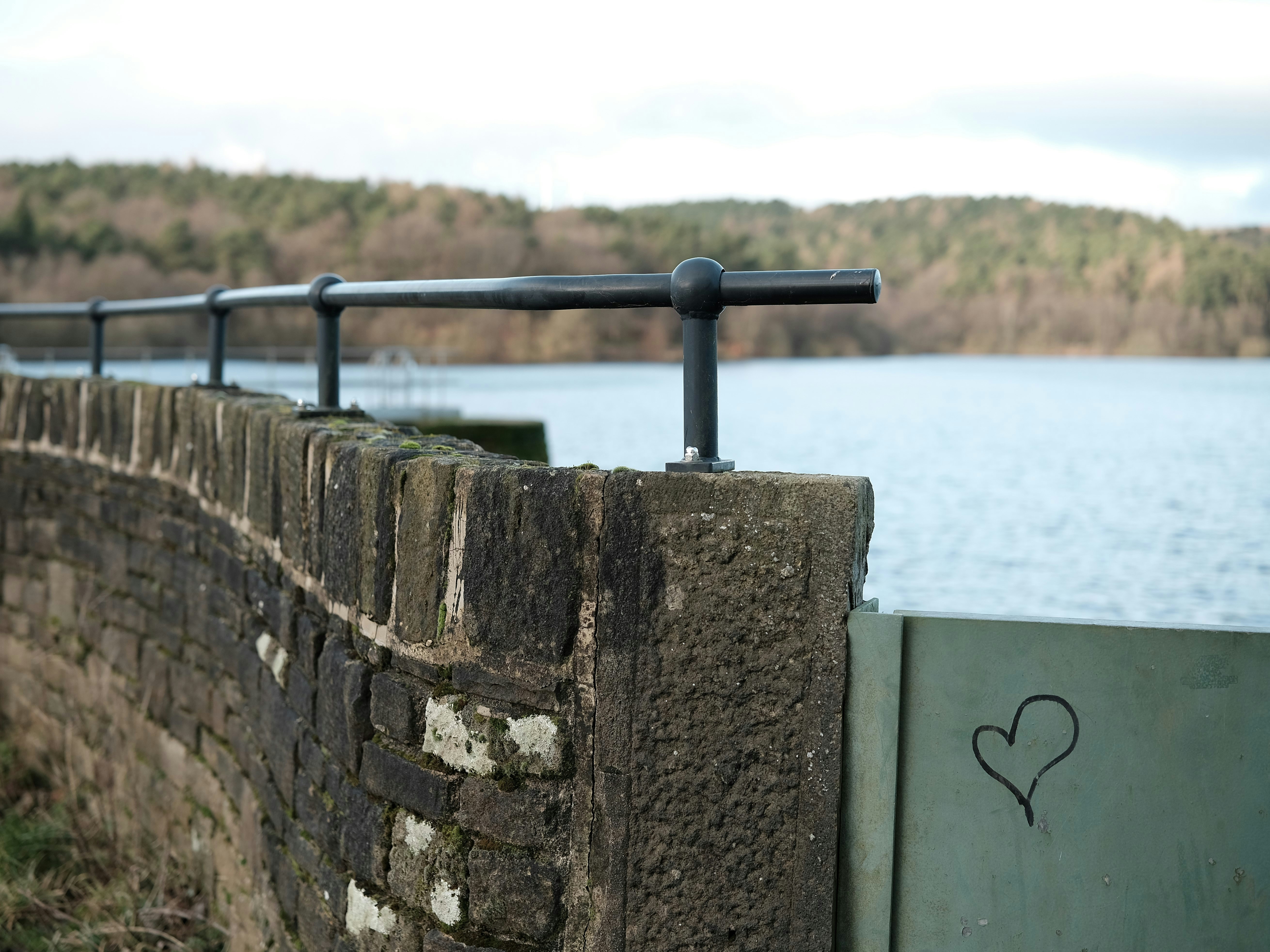 Weathered pier railing over calm lake with distant tree line