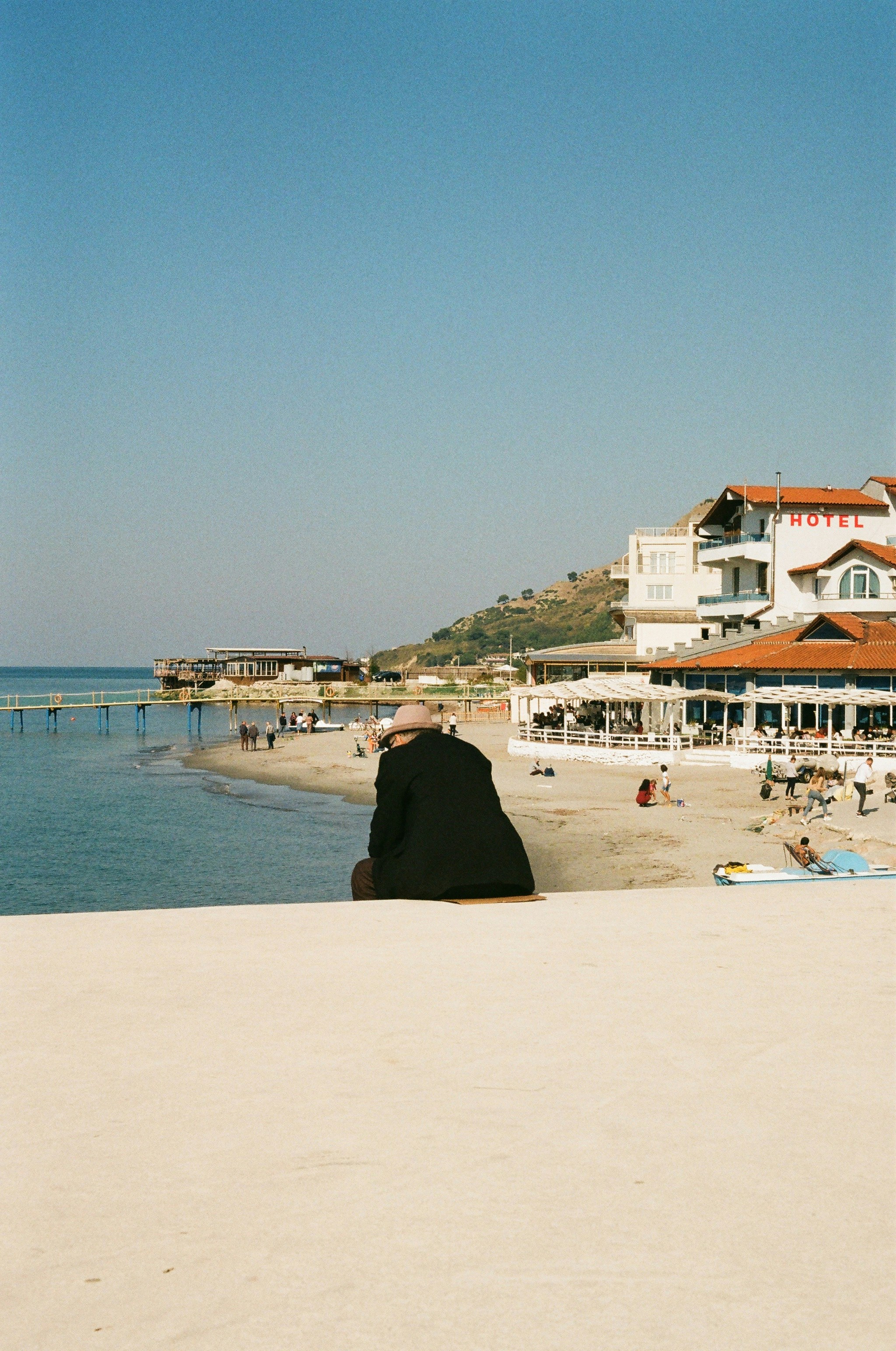 Lone silhouette on a sunlit seaside ledge amid a bustling coastal backdrop