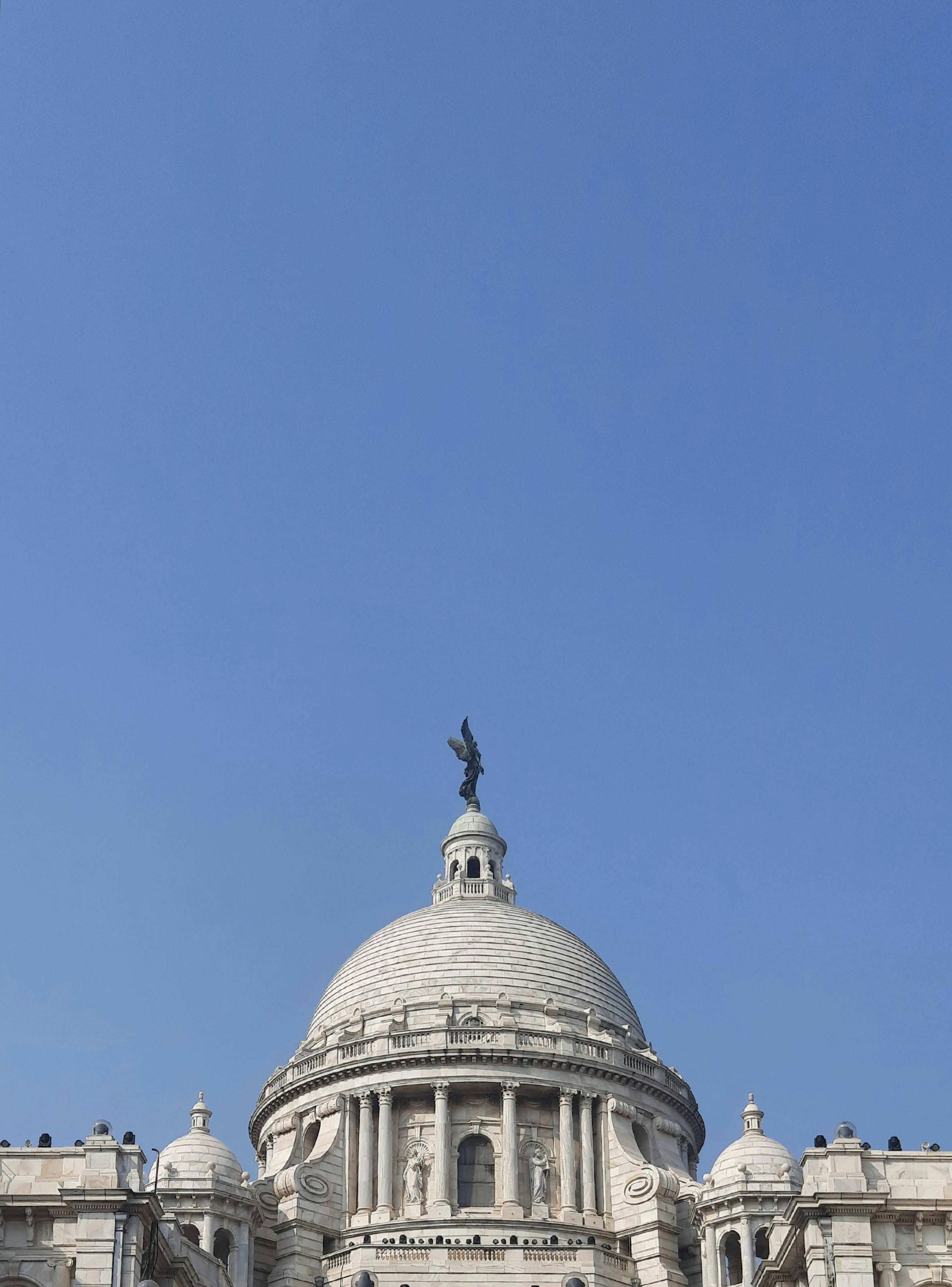 Architectural photograph of a grand domed capitol with a winged statue atop, set against a clear blue sky.