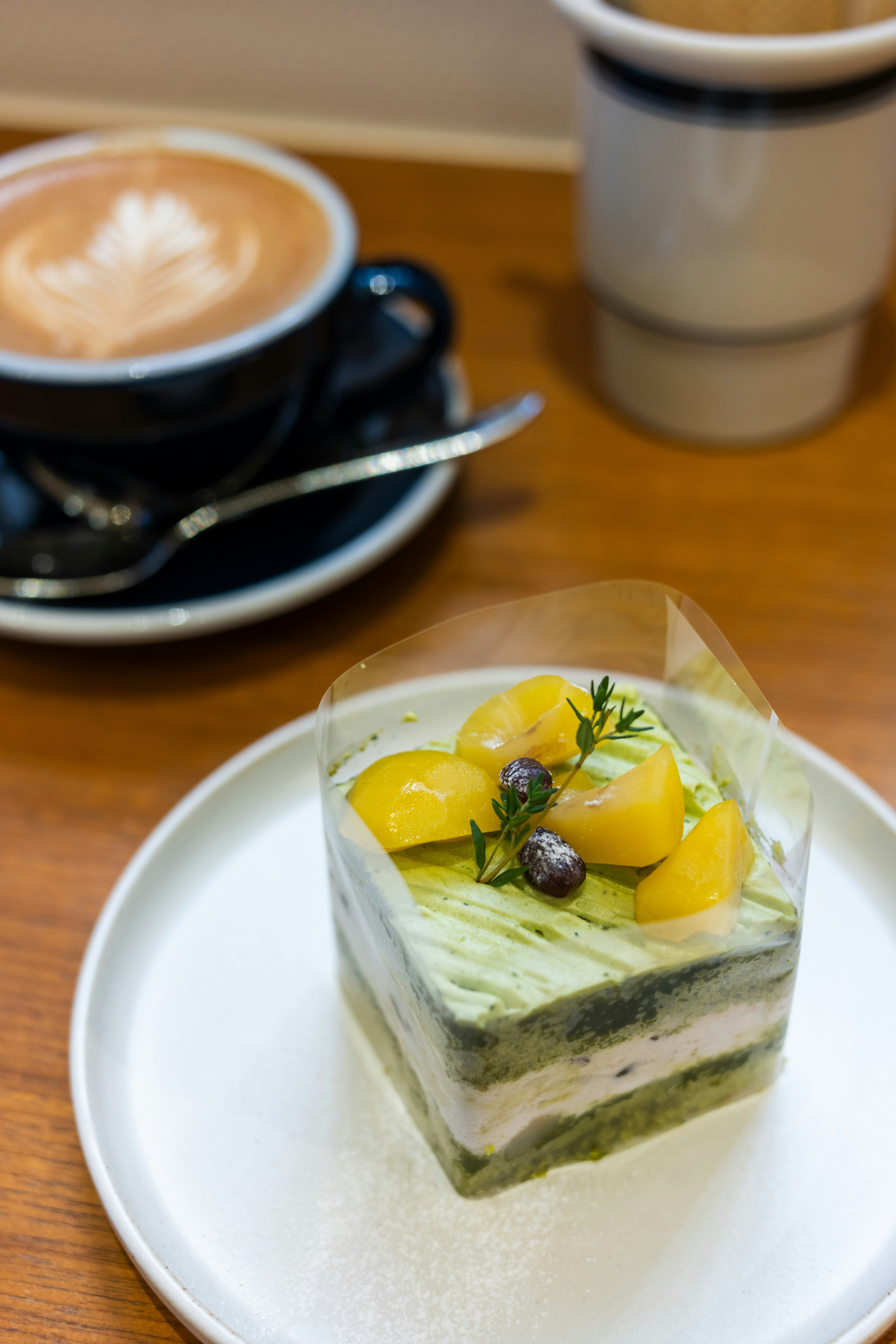 Minted Layers: A Green Tea Matcha Cake with Peach Garnish and a Foamy Café Scene
