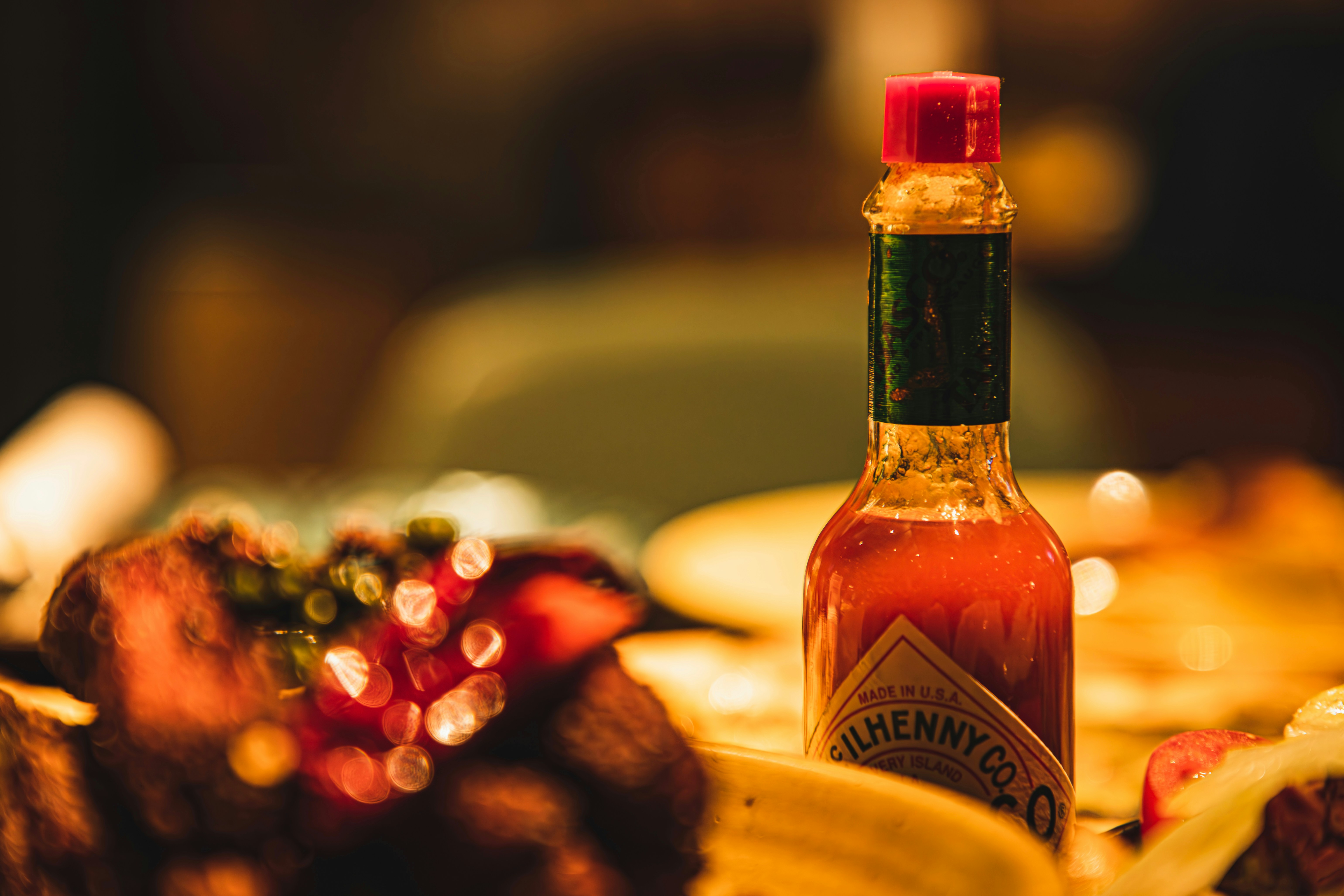 Amber heat on a wooden table: a lone hot sauce bottle amid blurred bounty