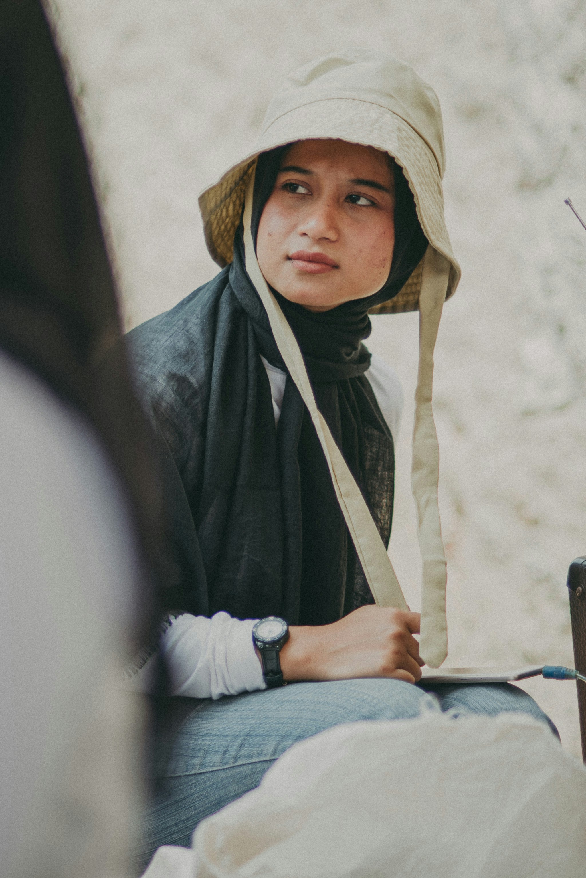 Une femme assise sur un banc, coiffée d’un chapeau et d’une écharpe ...