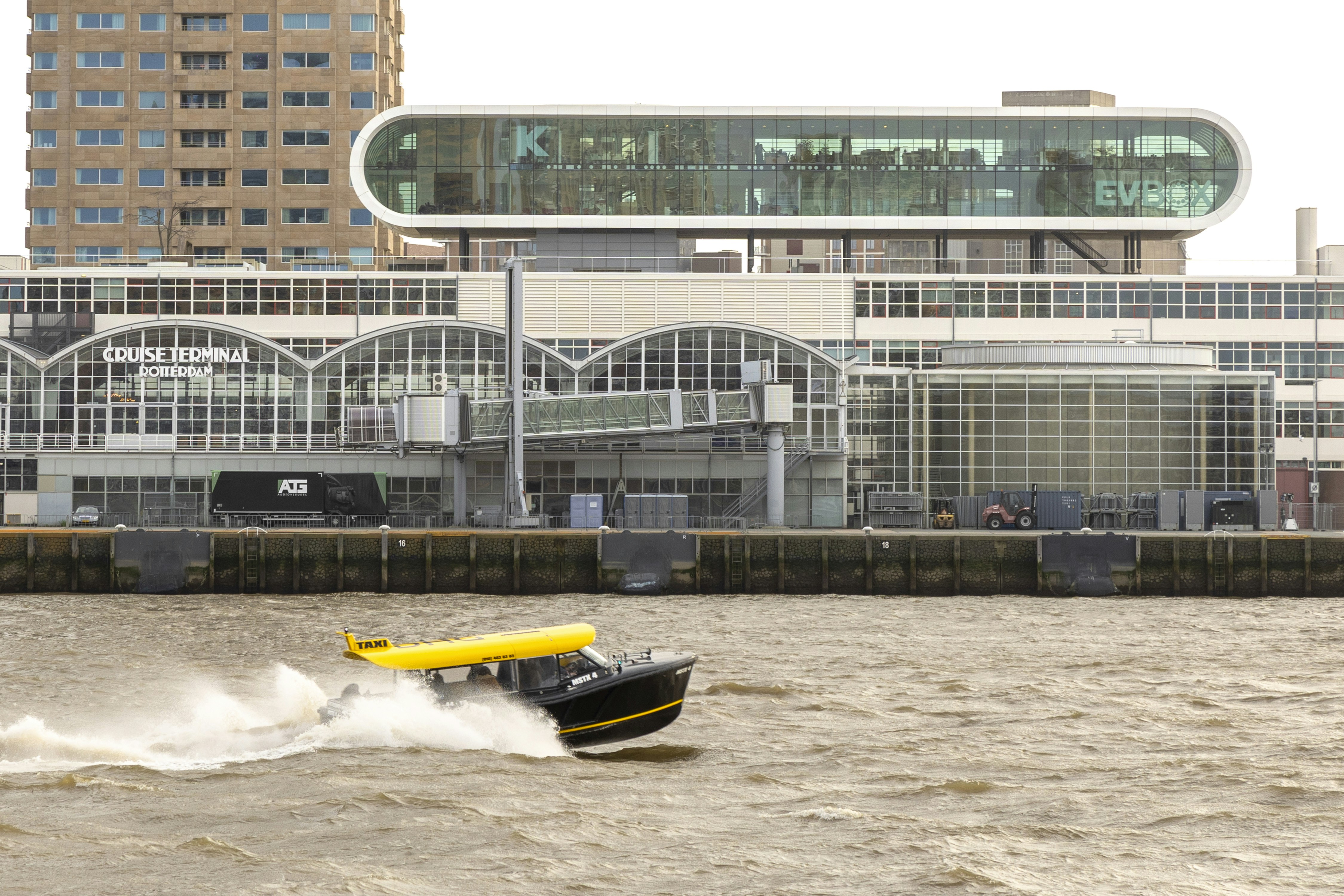 Wake and Glass: A Yellow Speedboat Dashes by a Futuristic Riverside