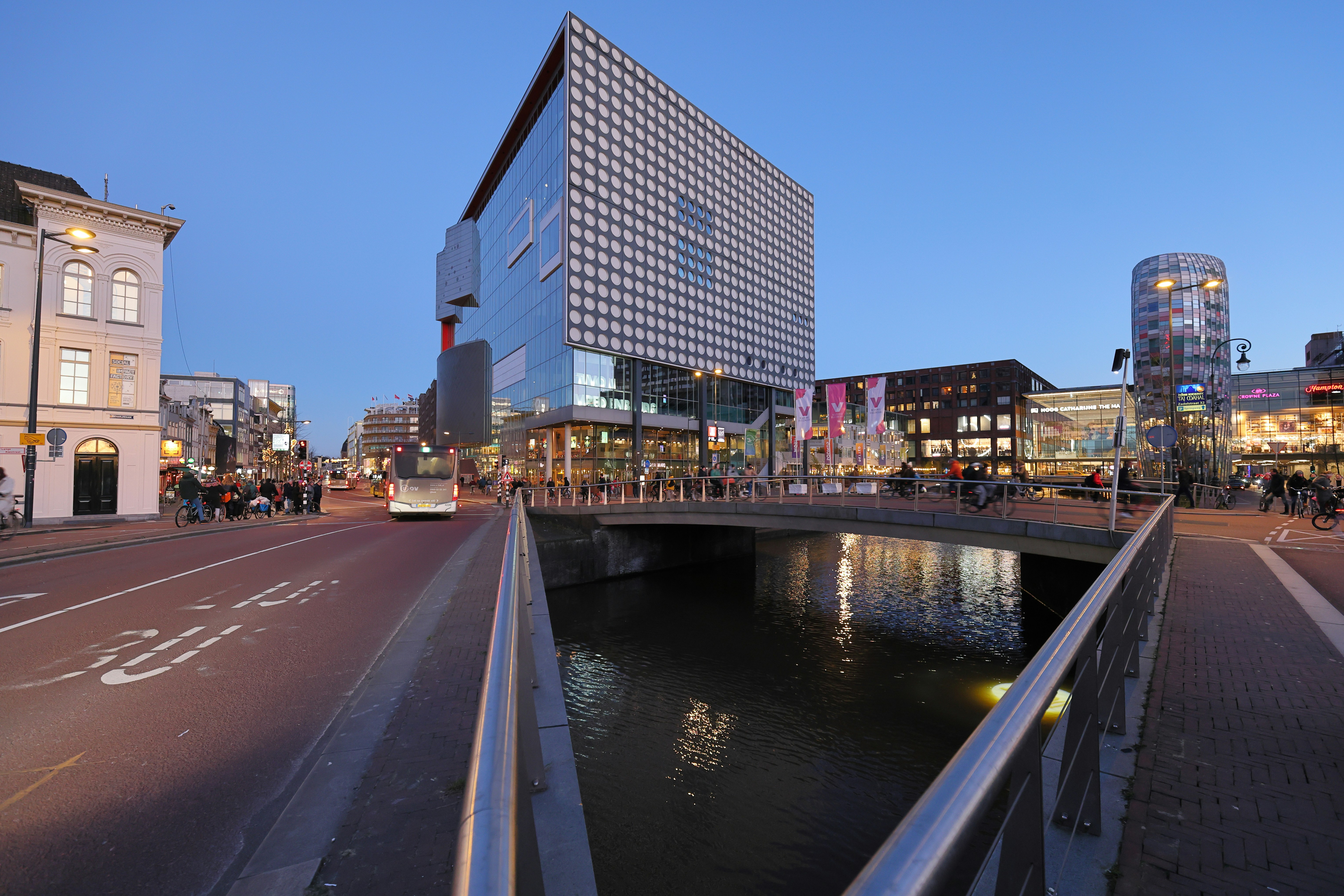 Modern cityscape with a unique patterned building and vibrant street life at dusk.
