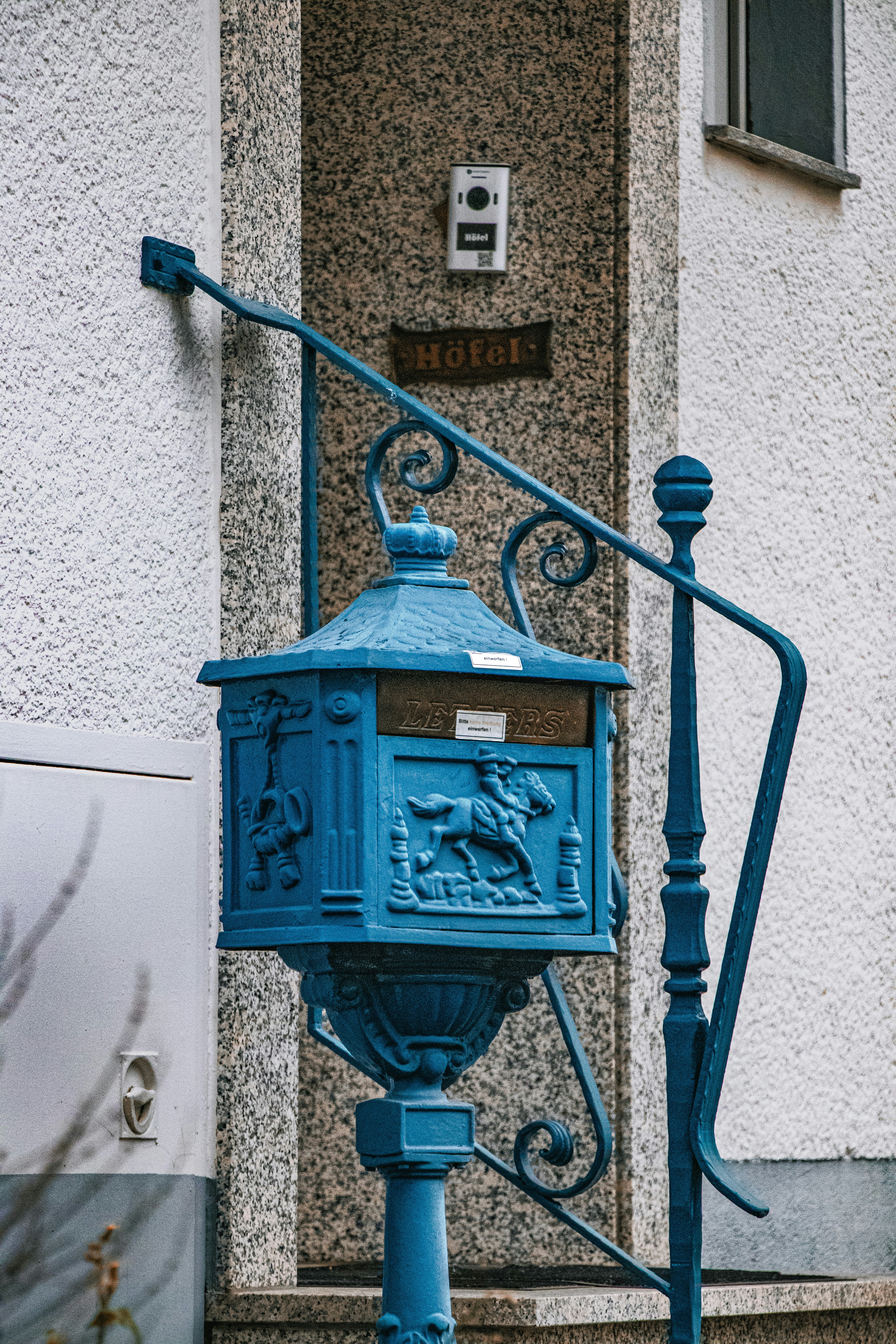 Blue Heritage Mailbox Amid Curved Ironwork on a Textured Facade