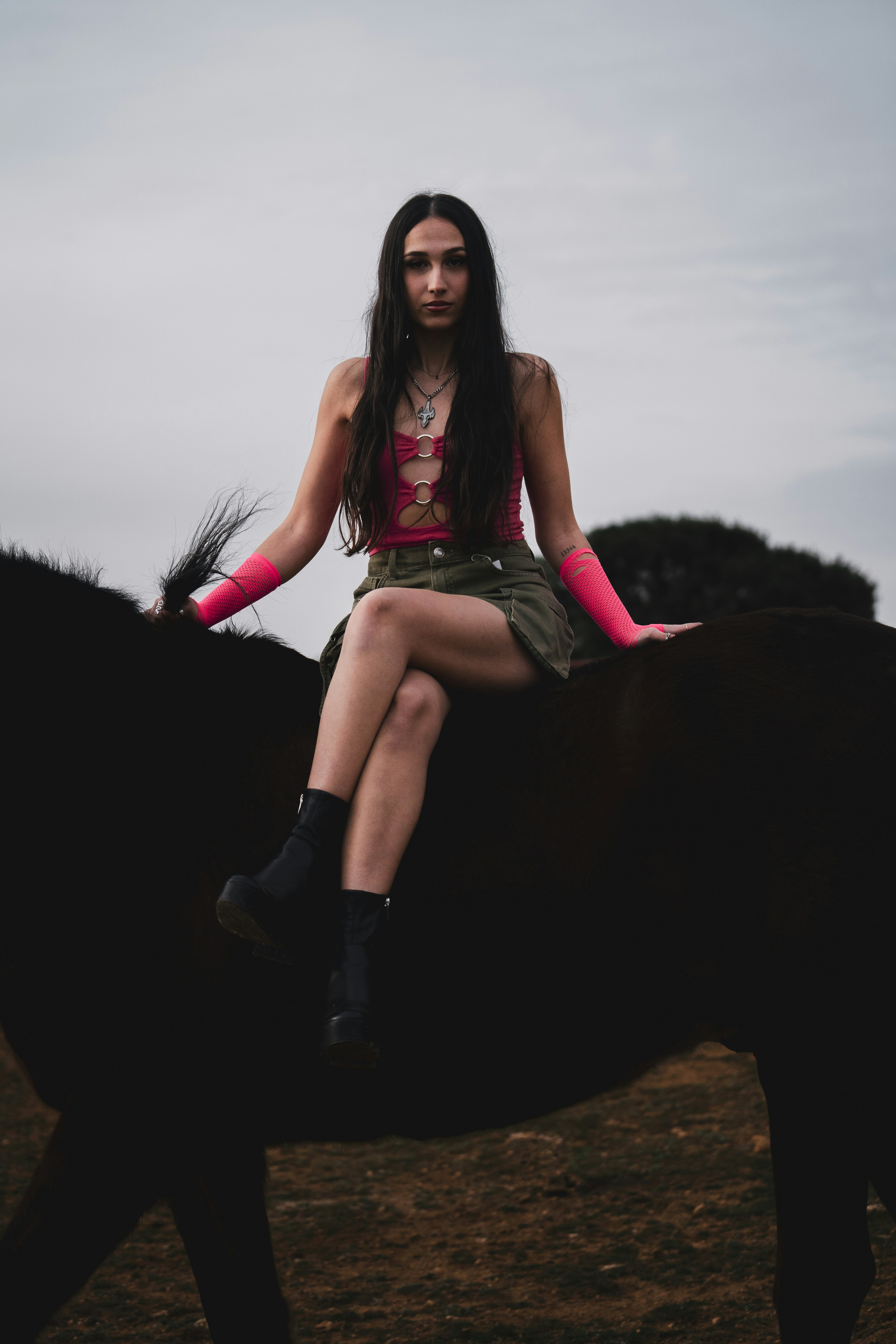 Woman in vibrant attire seated confidently on a dark horse against a muted sky.