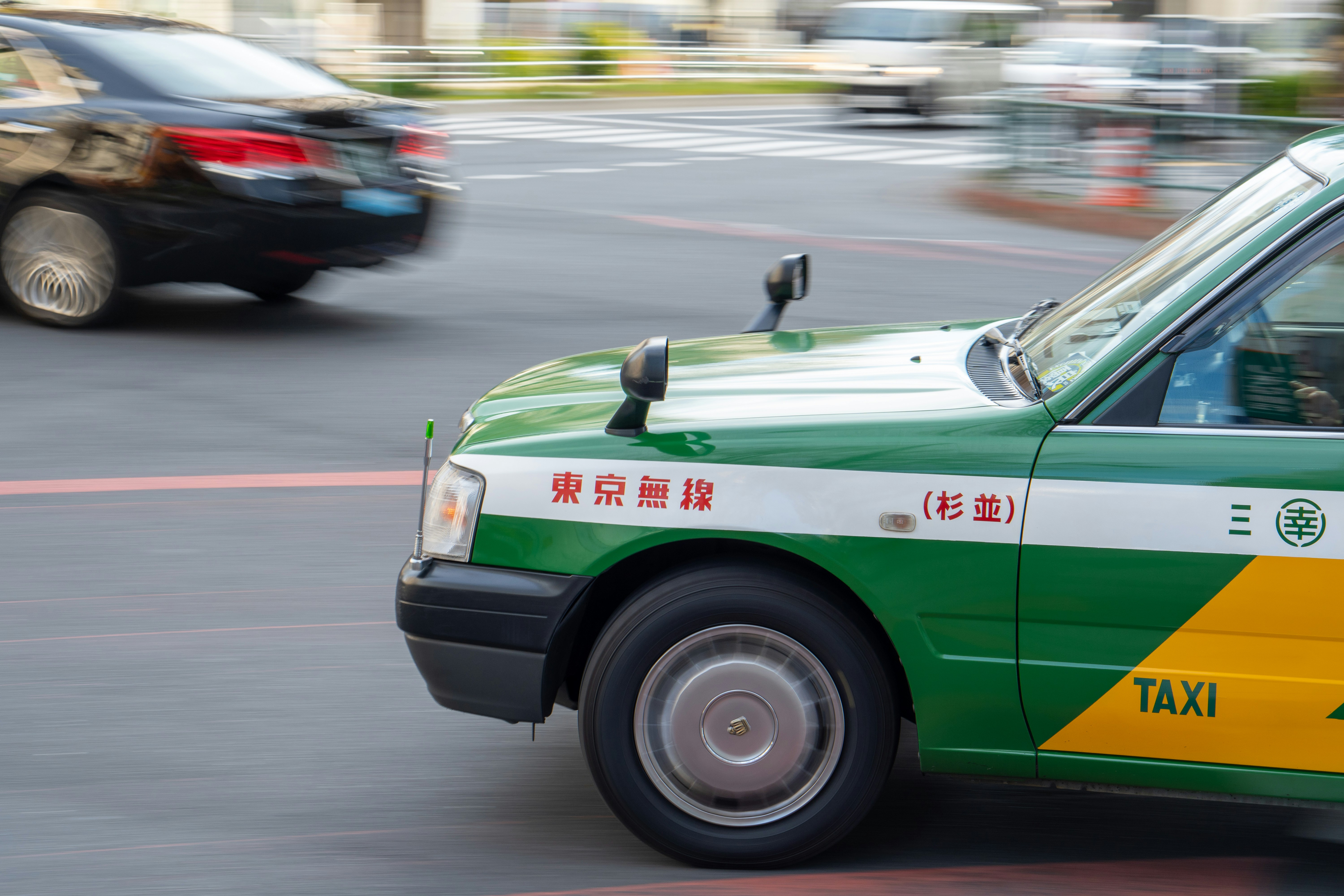 A taxi cab driving down a street next to a black car photo – Free Taxi ...