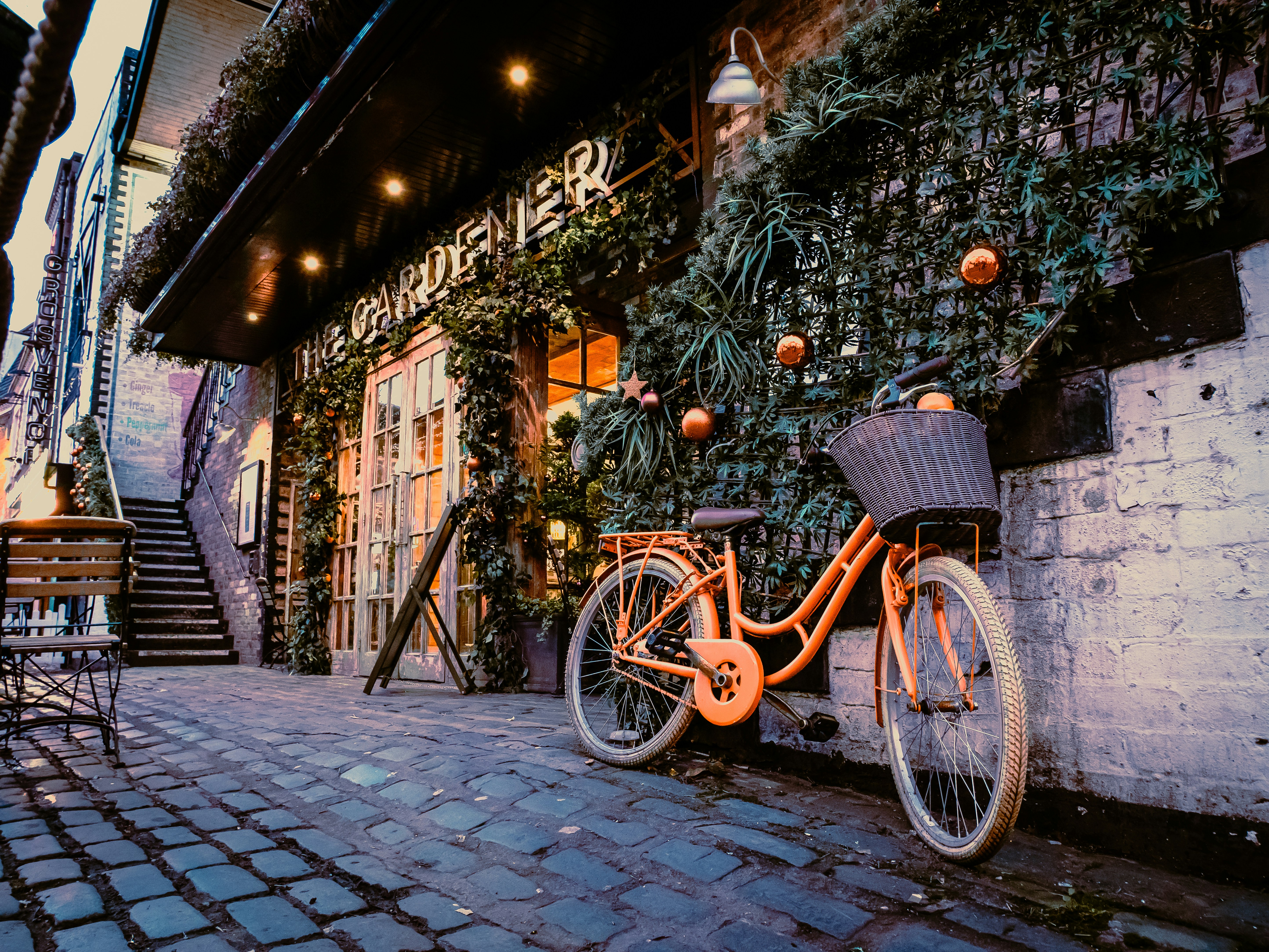 Orange bicycle with wicker basket parked along a cobblestone alley outside a warmly lit café.