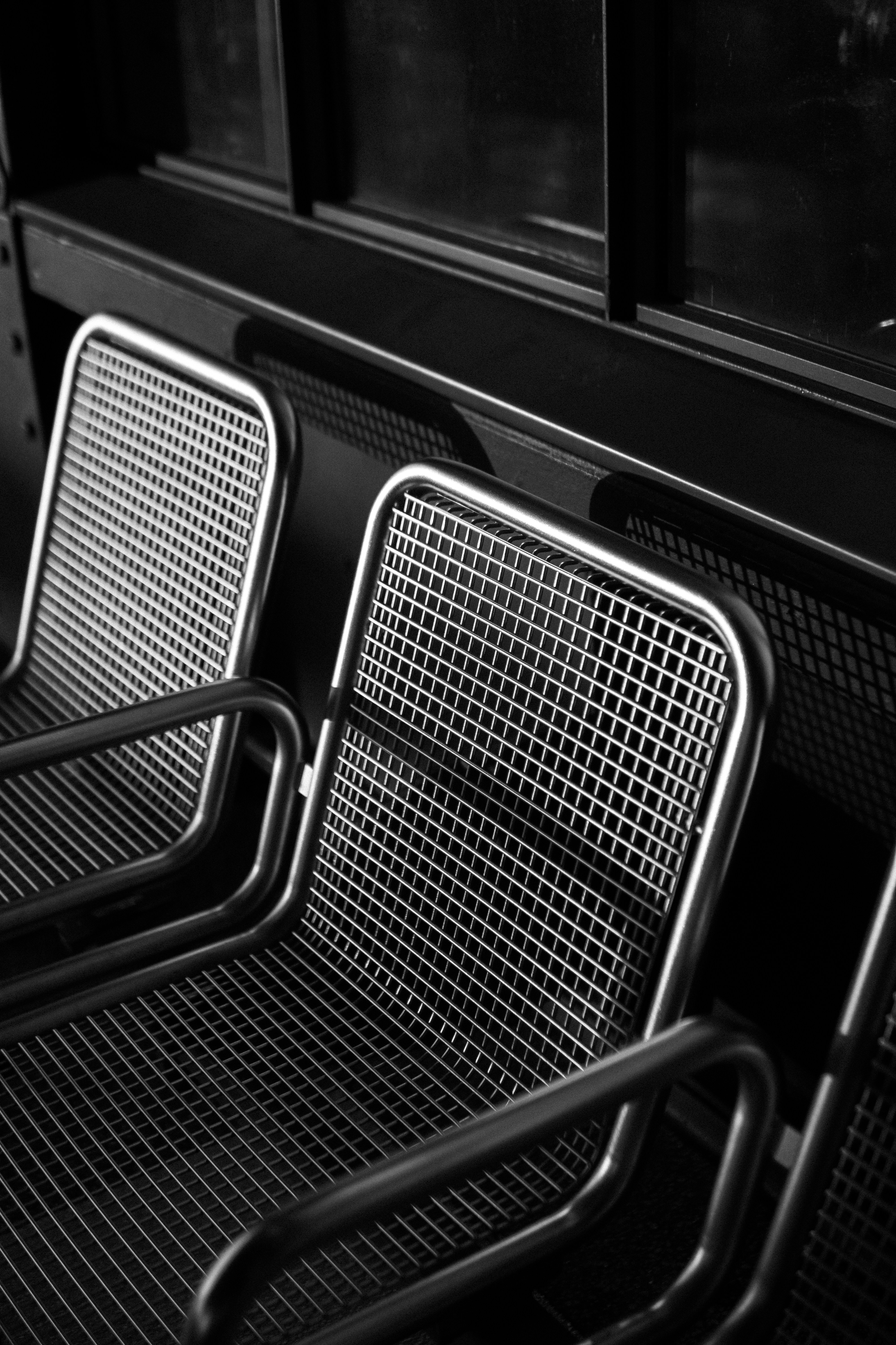 Captured in the heart of the city, this monochromatic image of chairs showcases the interplay of light and shadow upon the structured tranquility of urban design. The stark lines of the metal benches, arranged in a symmetrical pattern, offer a glimpse into the daily rhythm of public spaces. Each grid and curve tells a story of countless commuters who have paused here, if only for a moment.