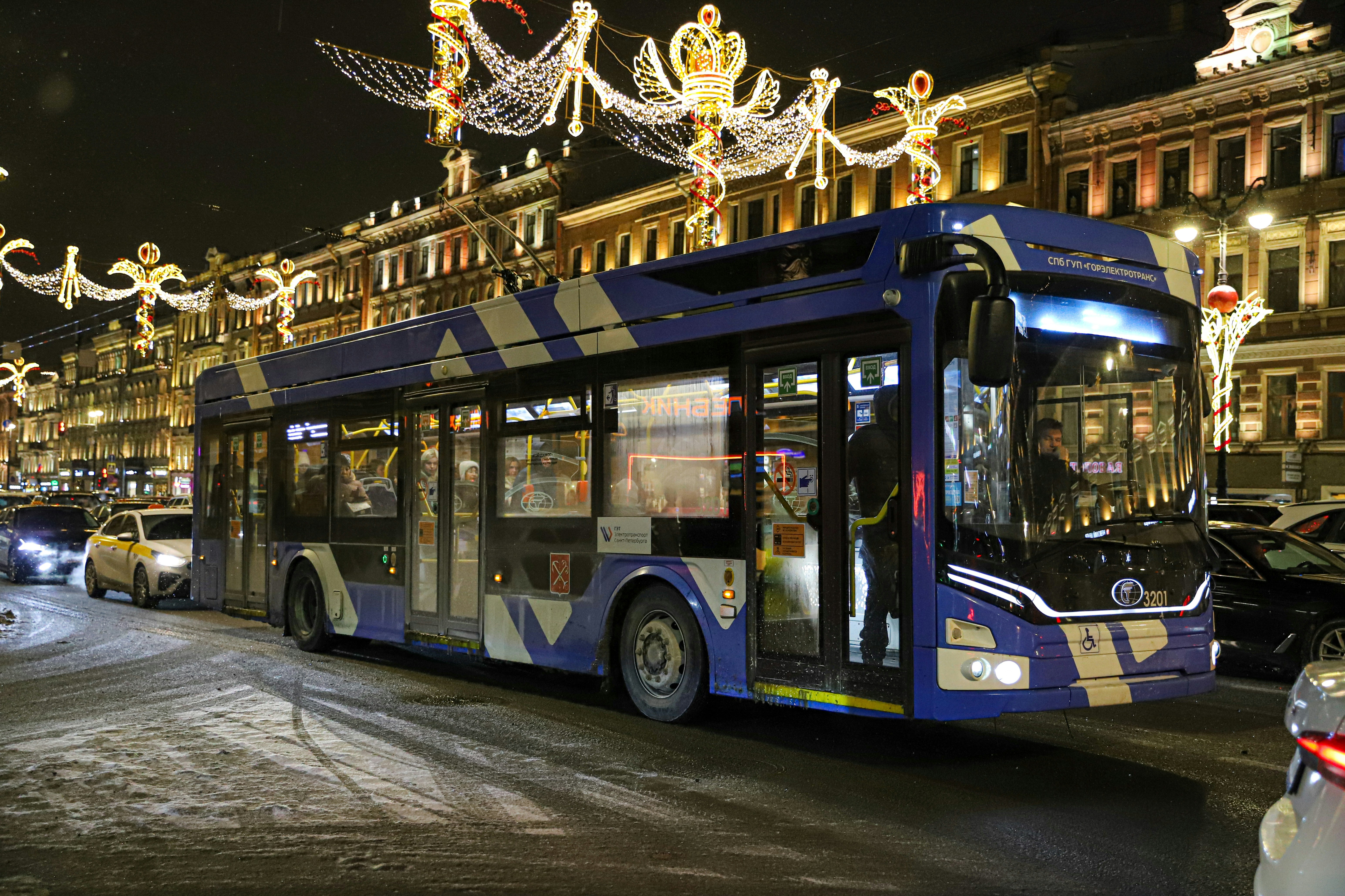 A blue bus driving down a street next to tall buildings photo – Free ...