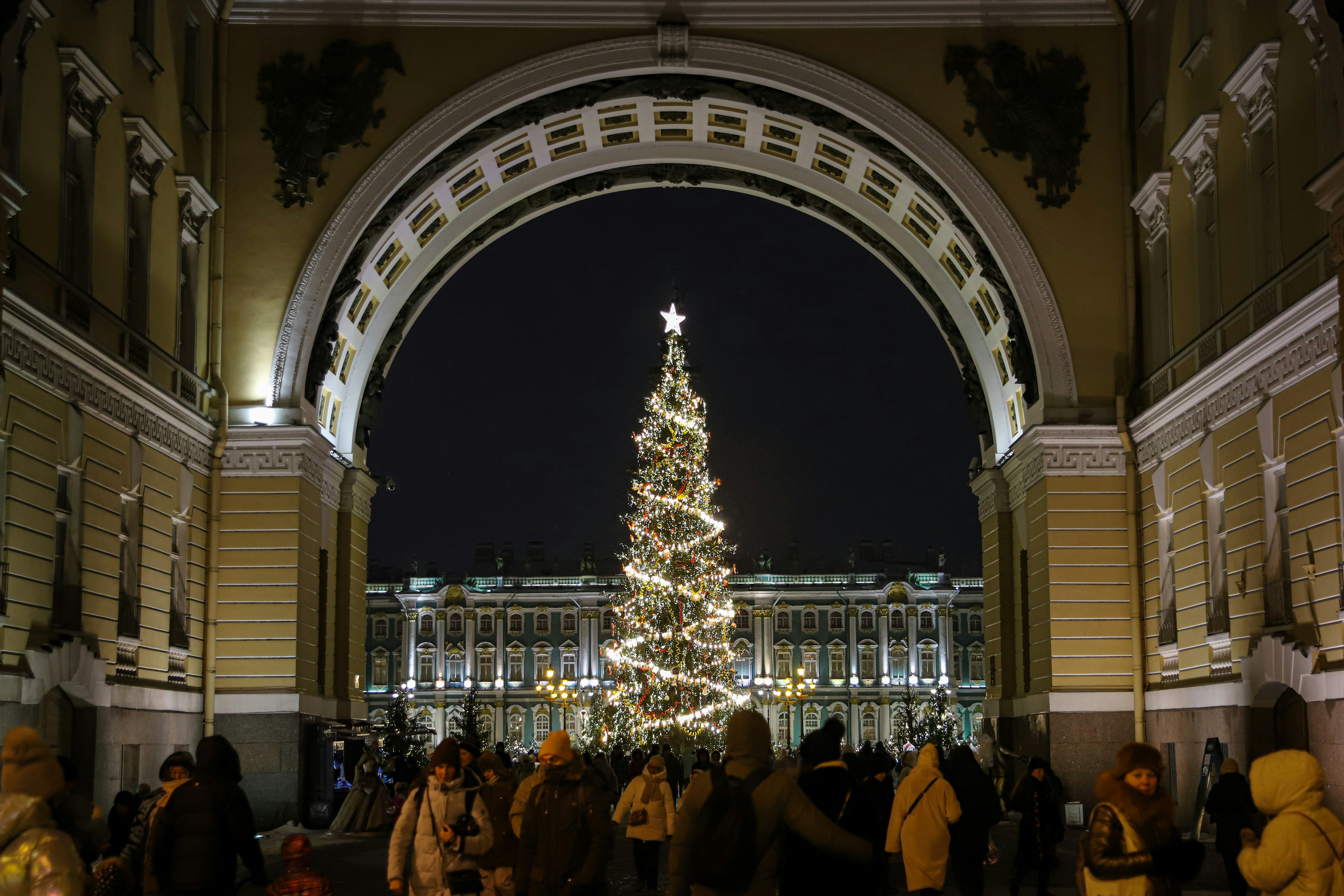 Illuminated Christmas tree beneath a grand archway with people gathered around.
