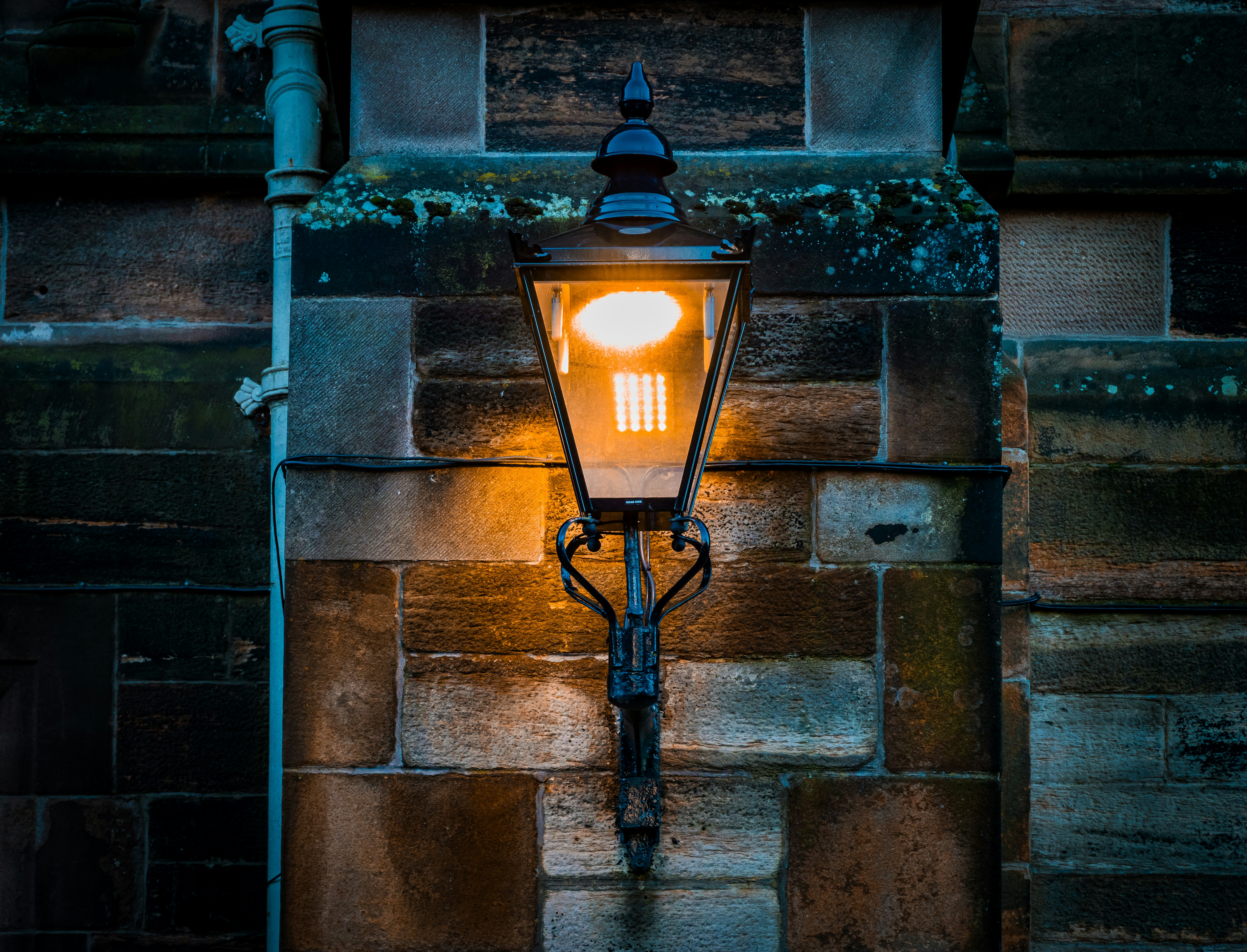 Warm glow from a vintage lantern mounted on a weathered brick wall at blue hour, captured in a moody photograph.