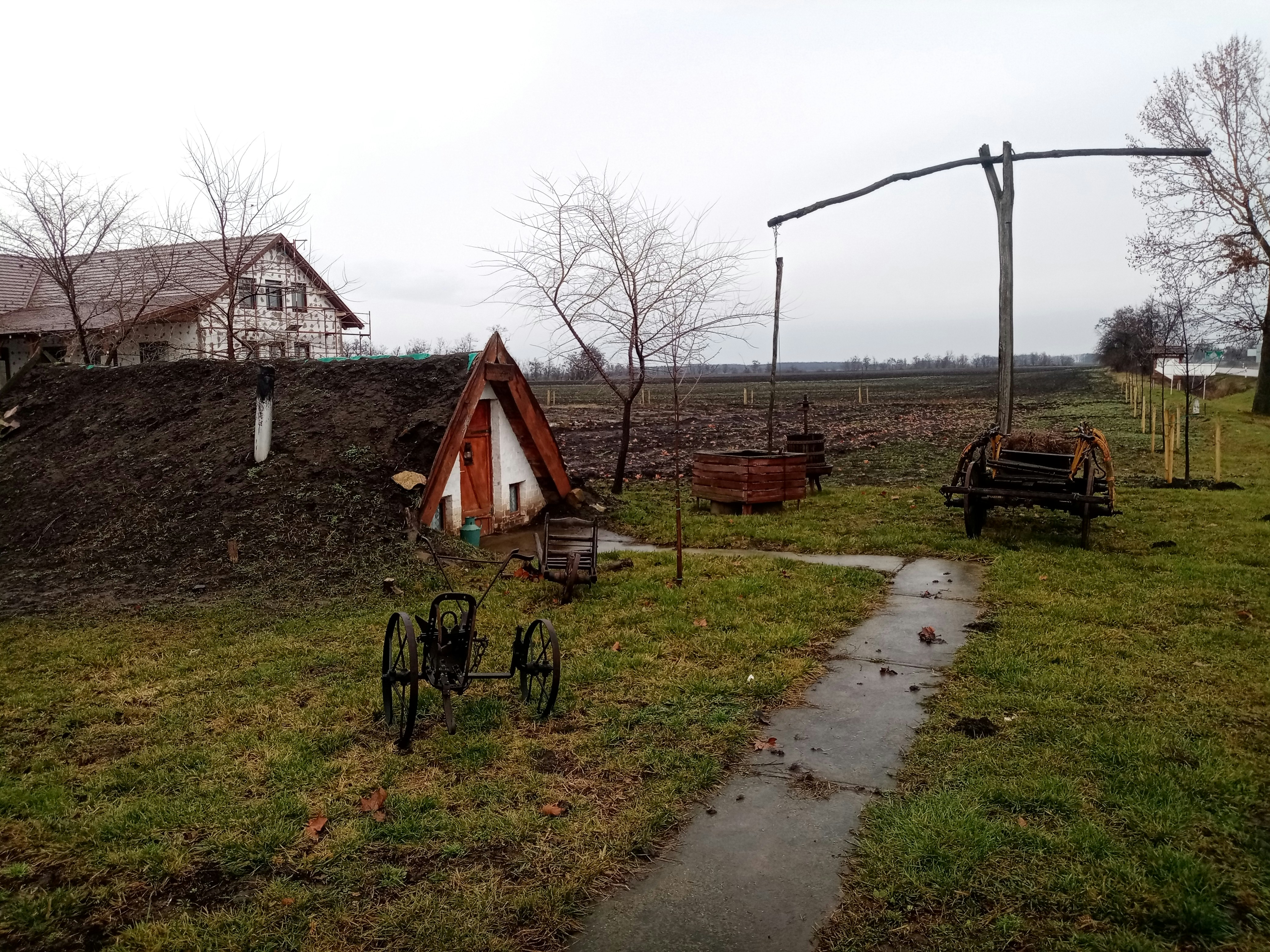 Rustic farm scene featuring an old wooden structure, vintage farming tools, and a muddy hill, evoking a sense of nostalgia for traditional agriculture.