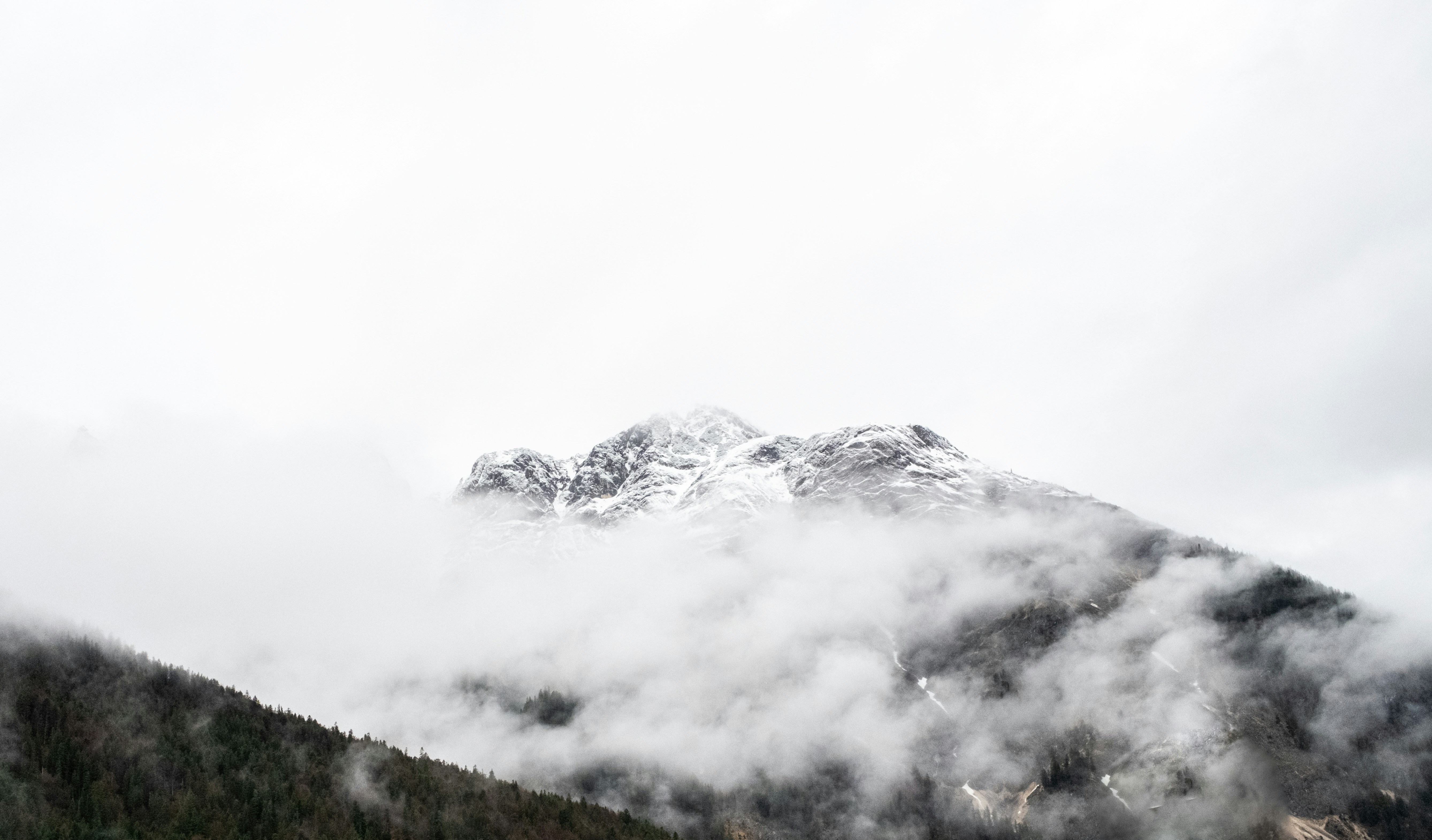 Snow-capped mountain peaks emerging from a thick blanket of clouds, creating a mystical atmosphere.