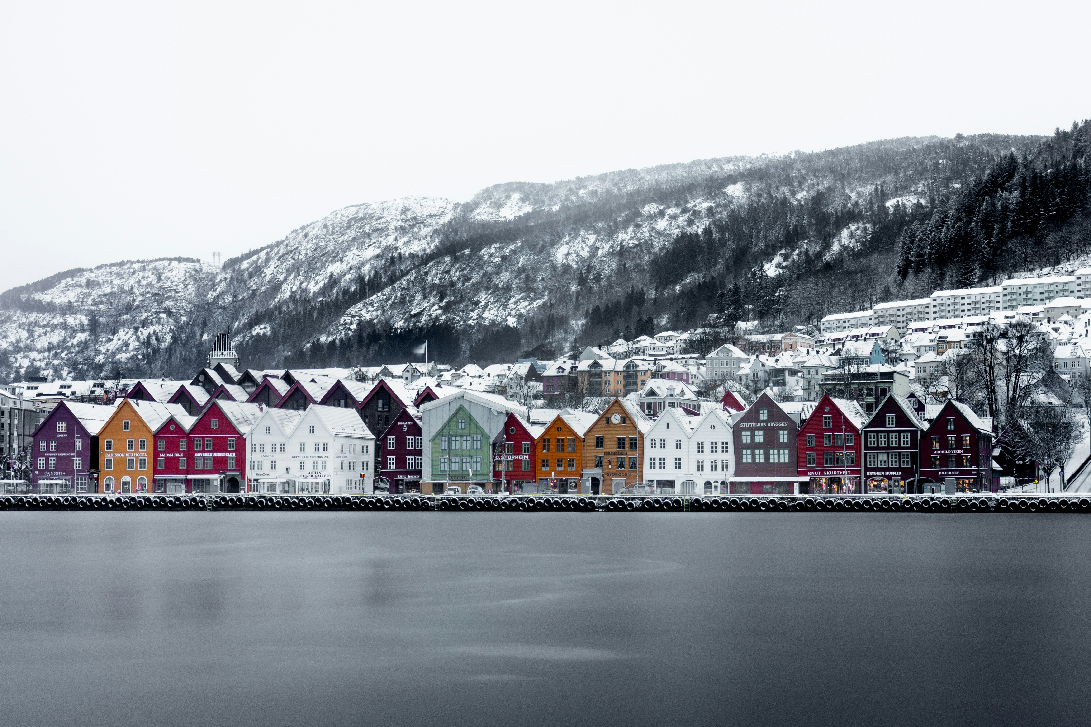 Colorful buildings line a snow-dusted harbor with mountains in the background.