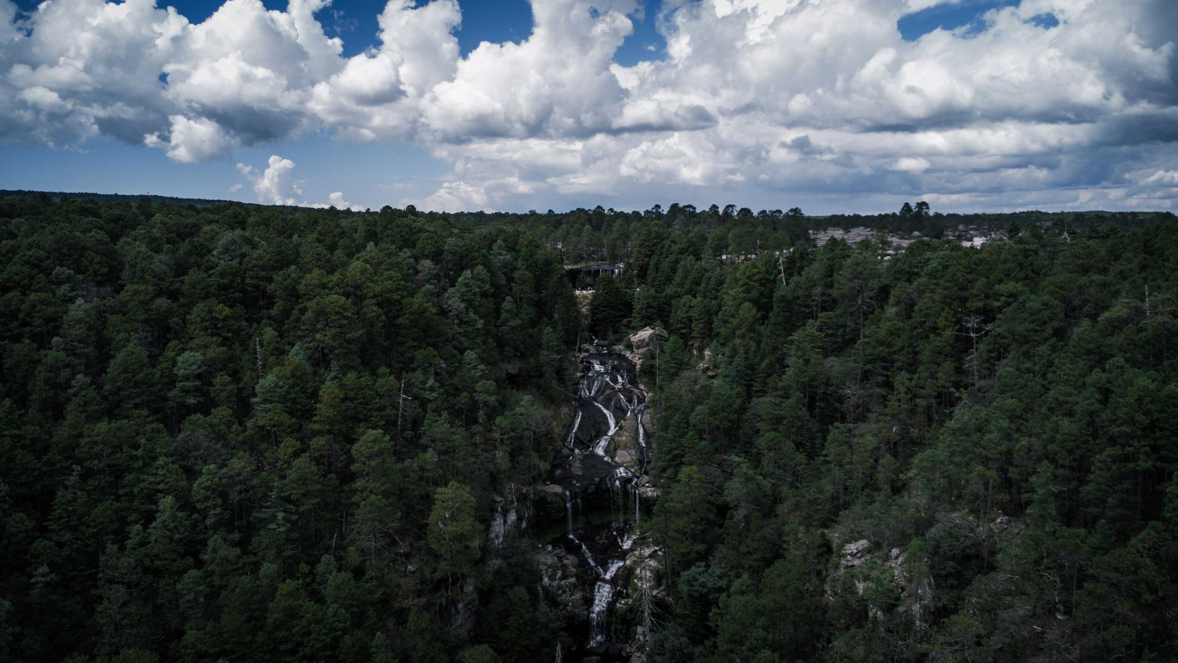 Waterfall flowing through dense forest under a sky filled with dramatic clouds.