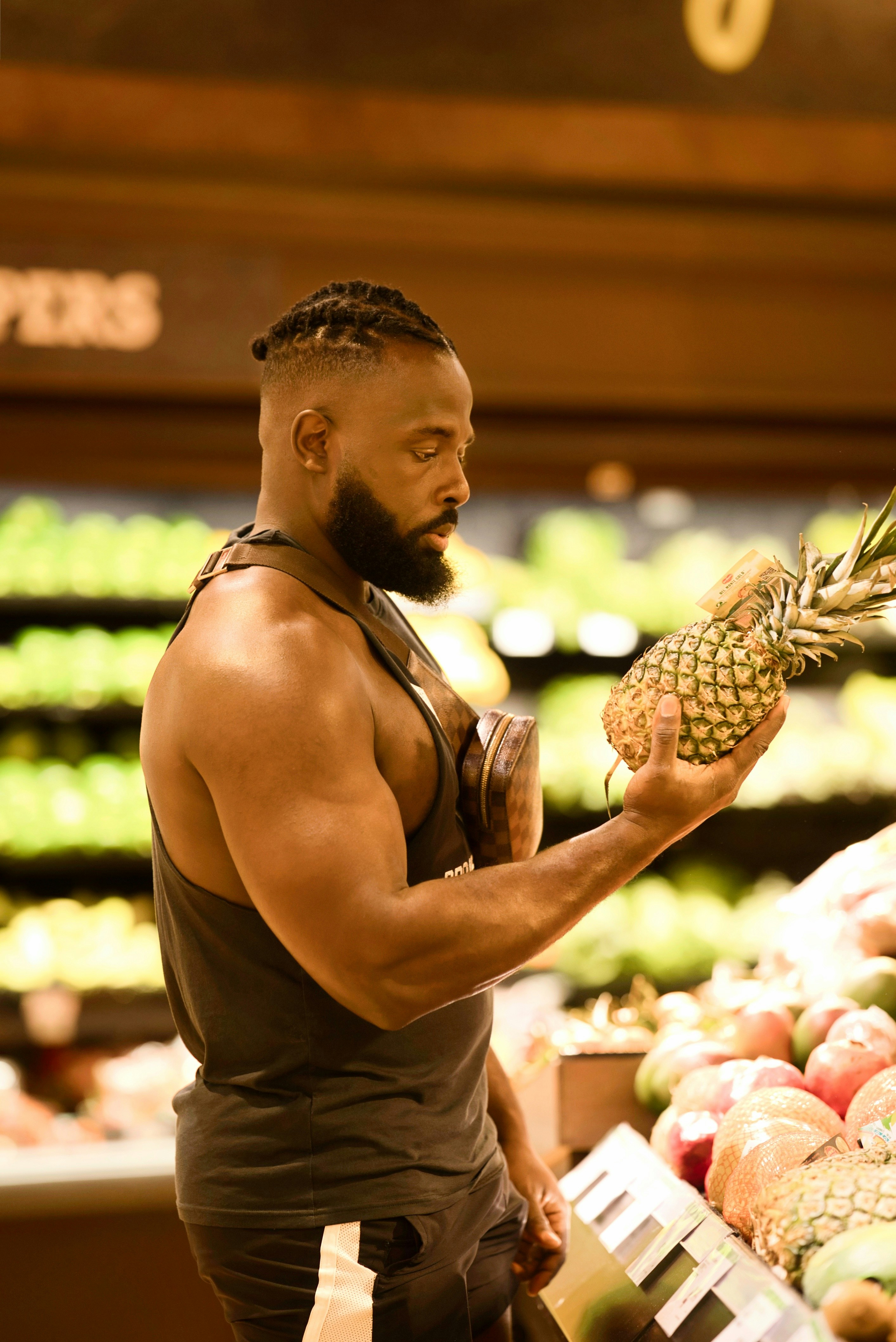 Produce Aisle Contemplation: a muscular shopper weighs a pineapple.