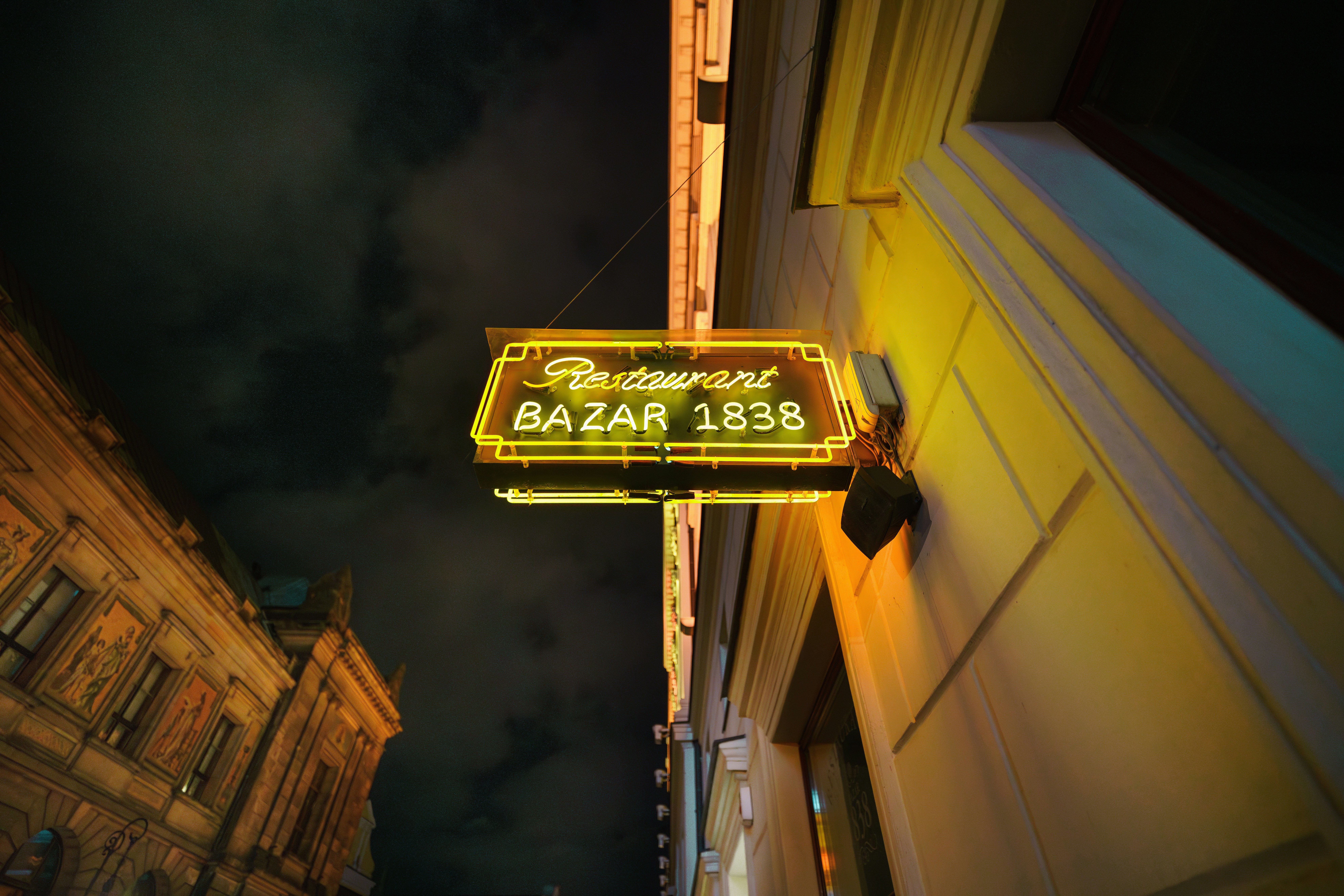 Neon sign for 'Bazar 1335' hangs from a building, illuminated against a dark night sky.