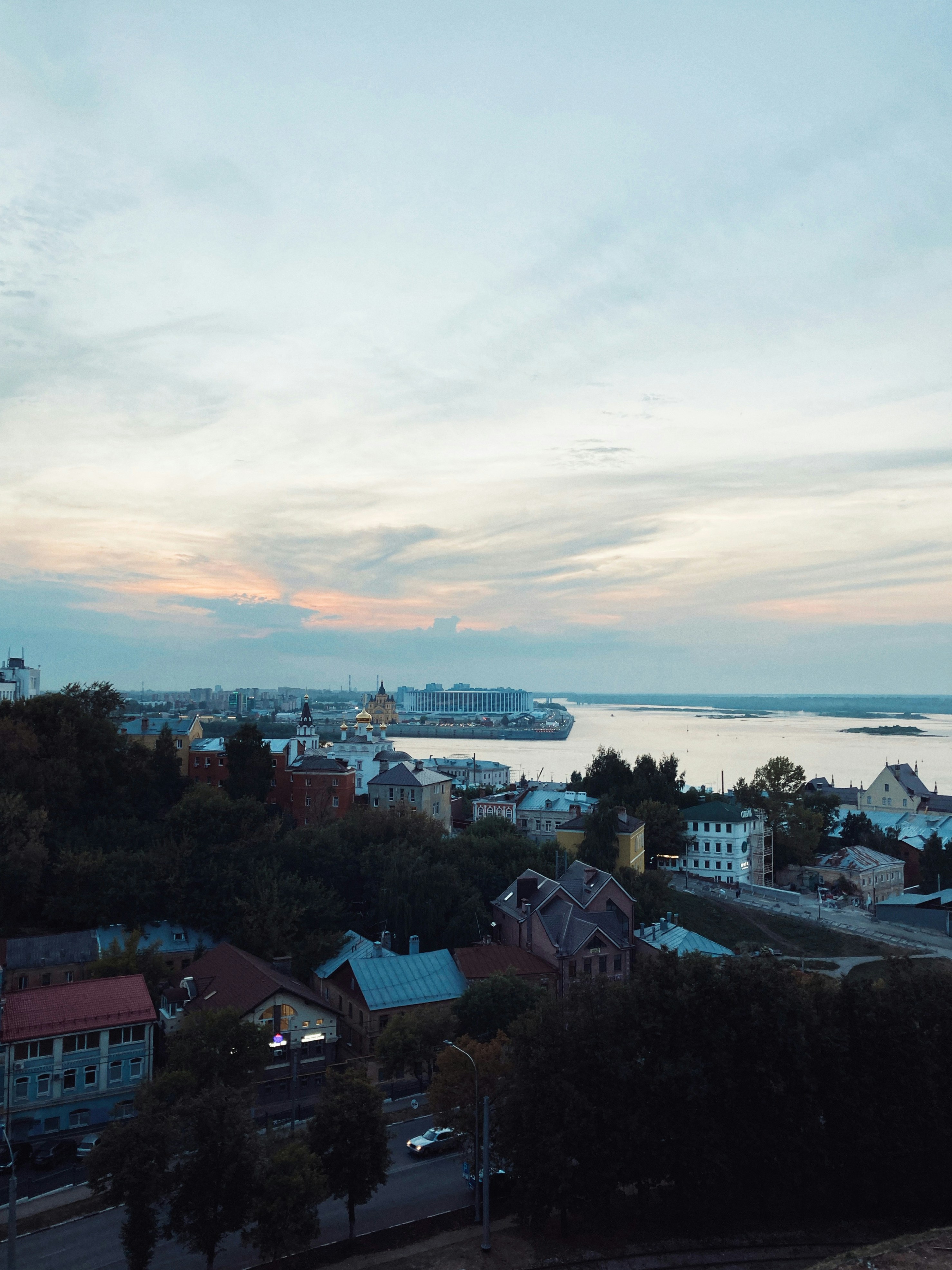 A tranquil riverside town at dusk with pastel skies and distant cityscape.