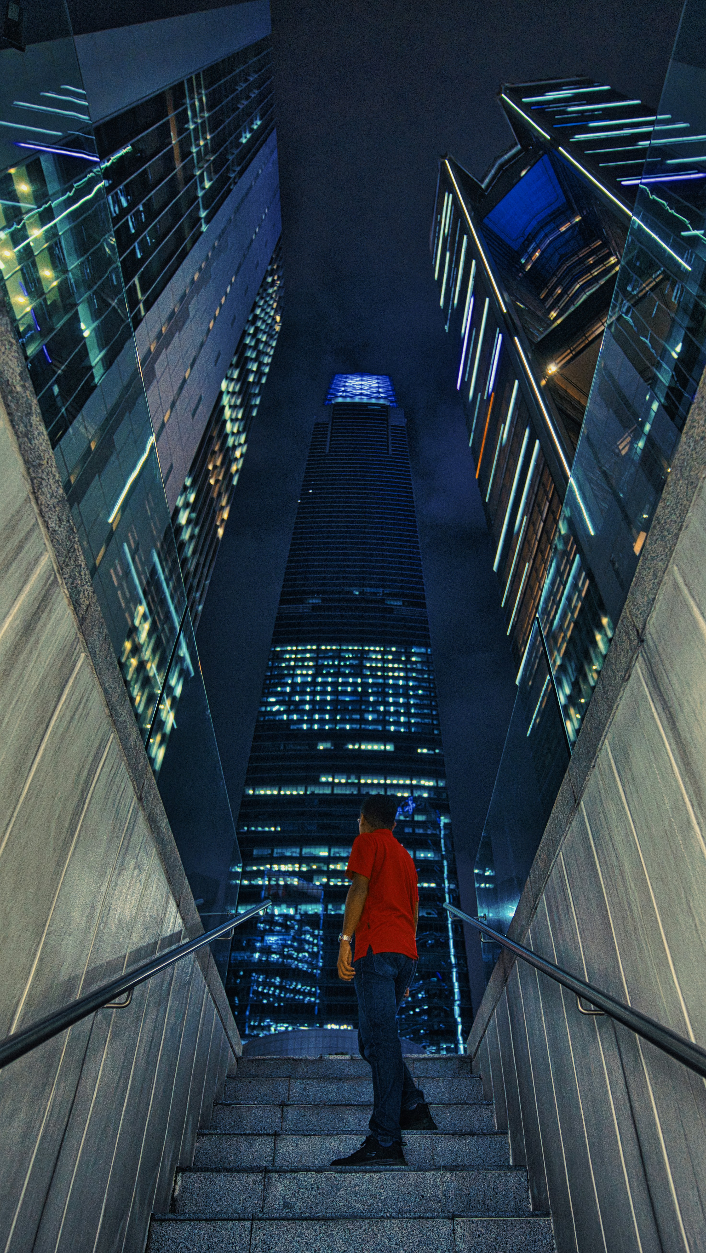 Neon Stairwell: A Red-Shirted Figure Beneath the Glass Giants