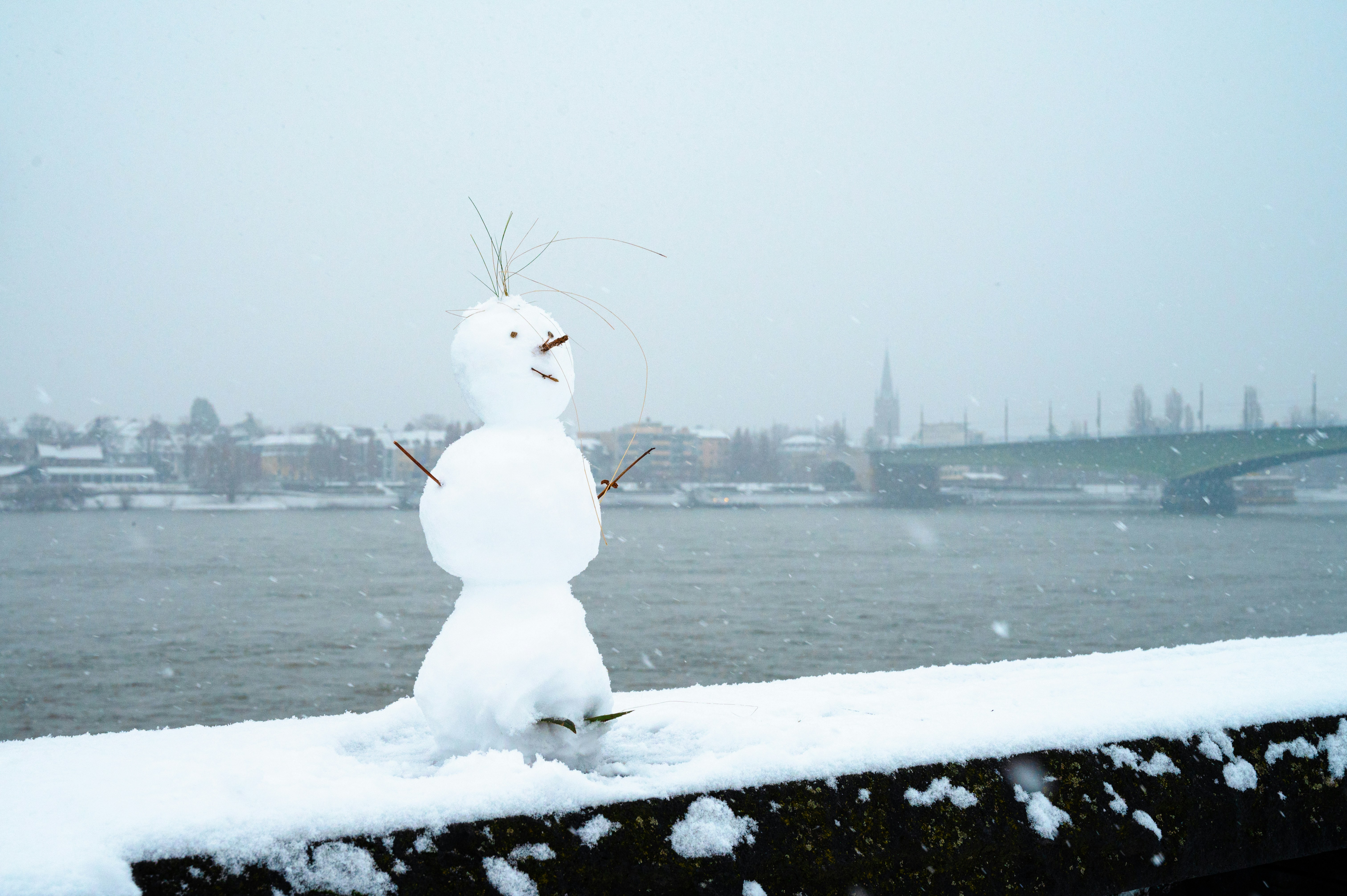 Snowman Sentinel Over a Snow-Dusted Riverfront City