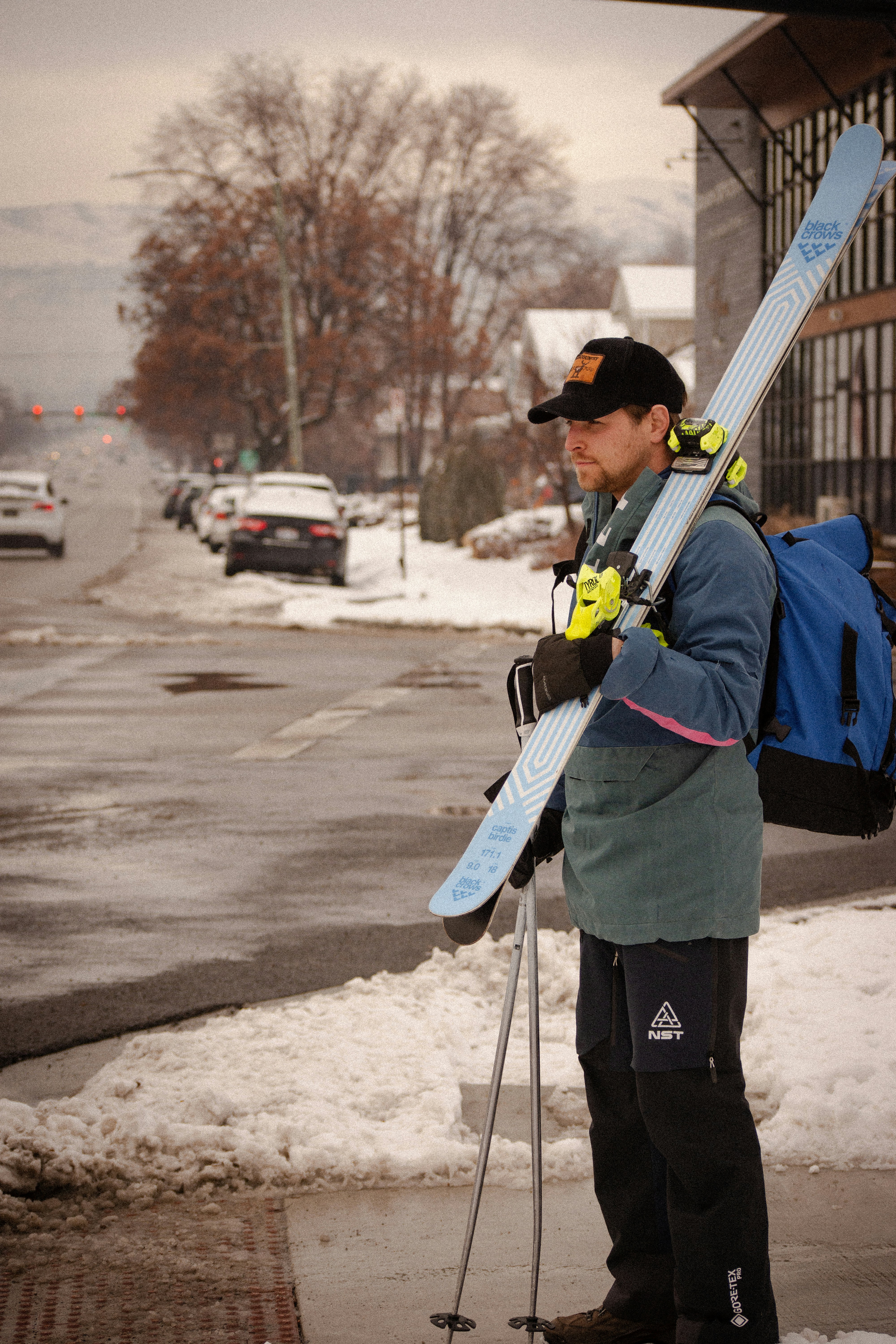 Snowbound Street Stop: A Skier Pauses with Alpine Gear in an Urban Landscape