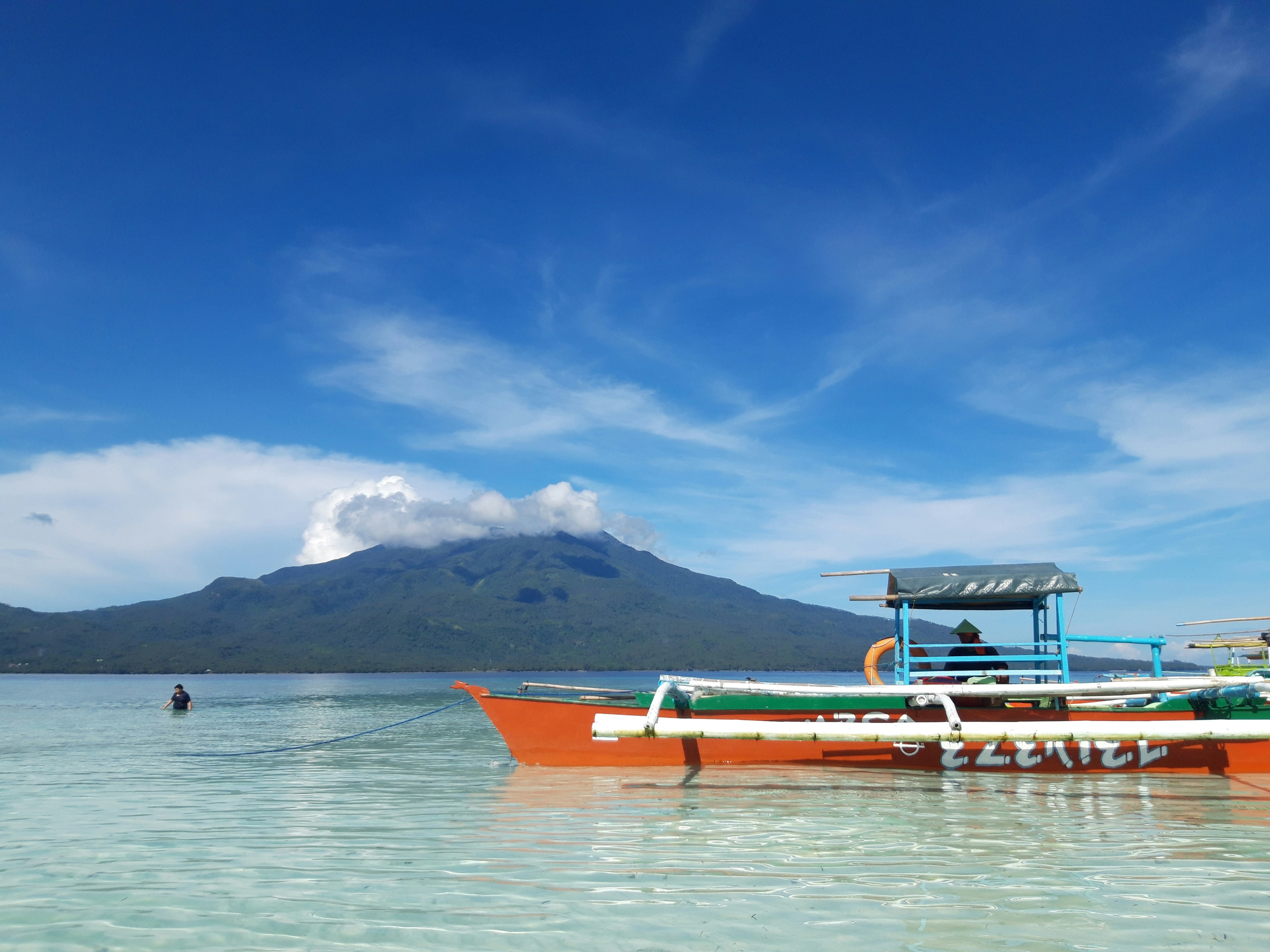 Clay-Red Boat at the Edge of a Turquoise Lagoon with a Volcanic Backdrop