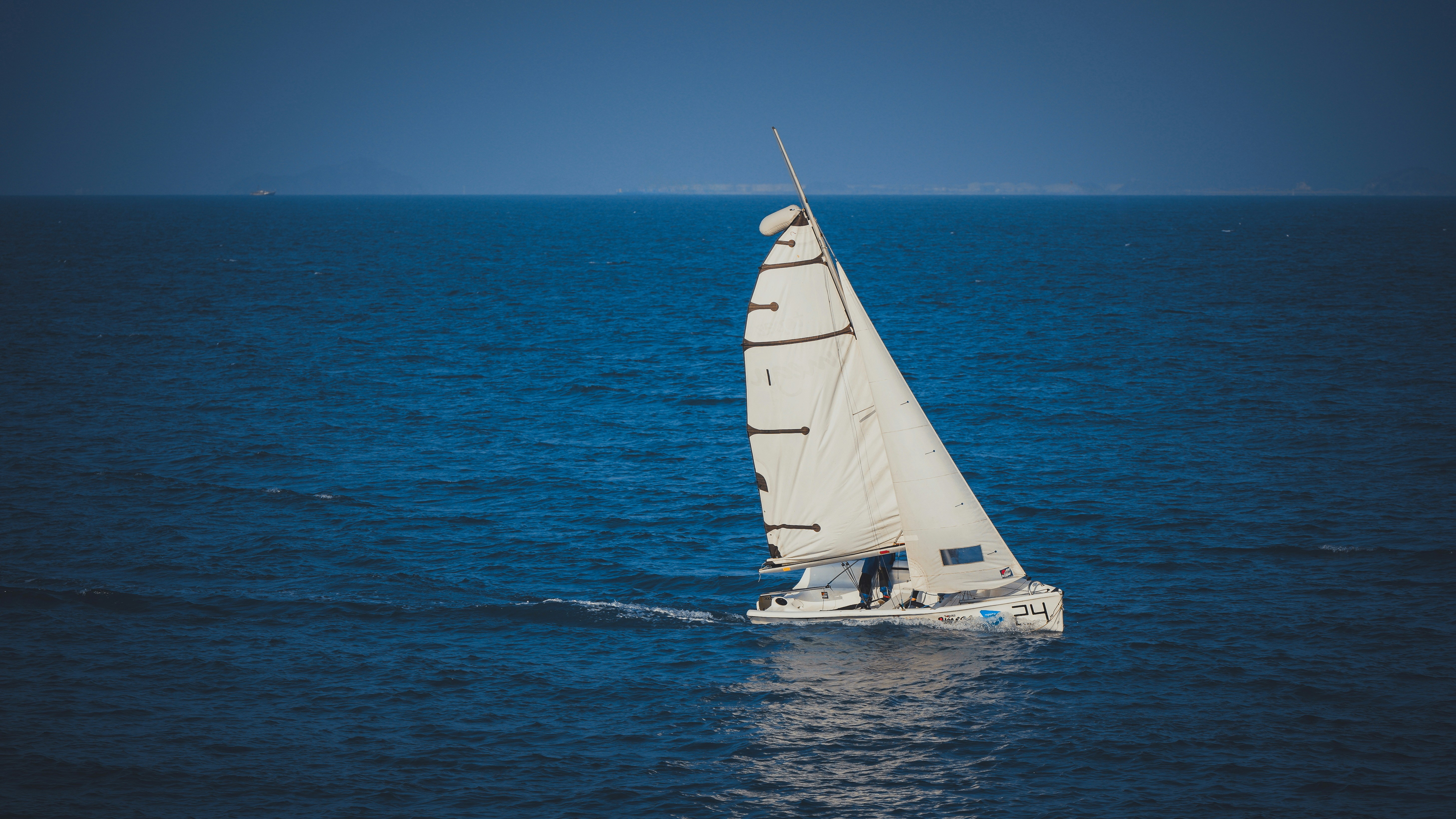 Sailboat gliding gracefully across deep blue waters under a clear sky. The scene captures the essence of tranquility and adventure.