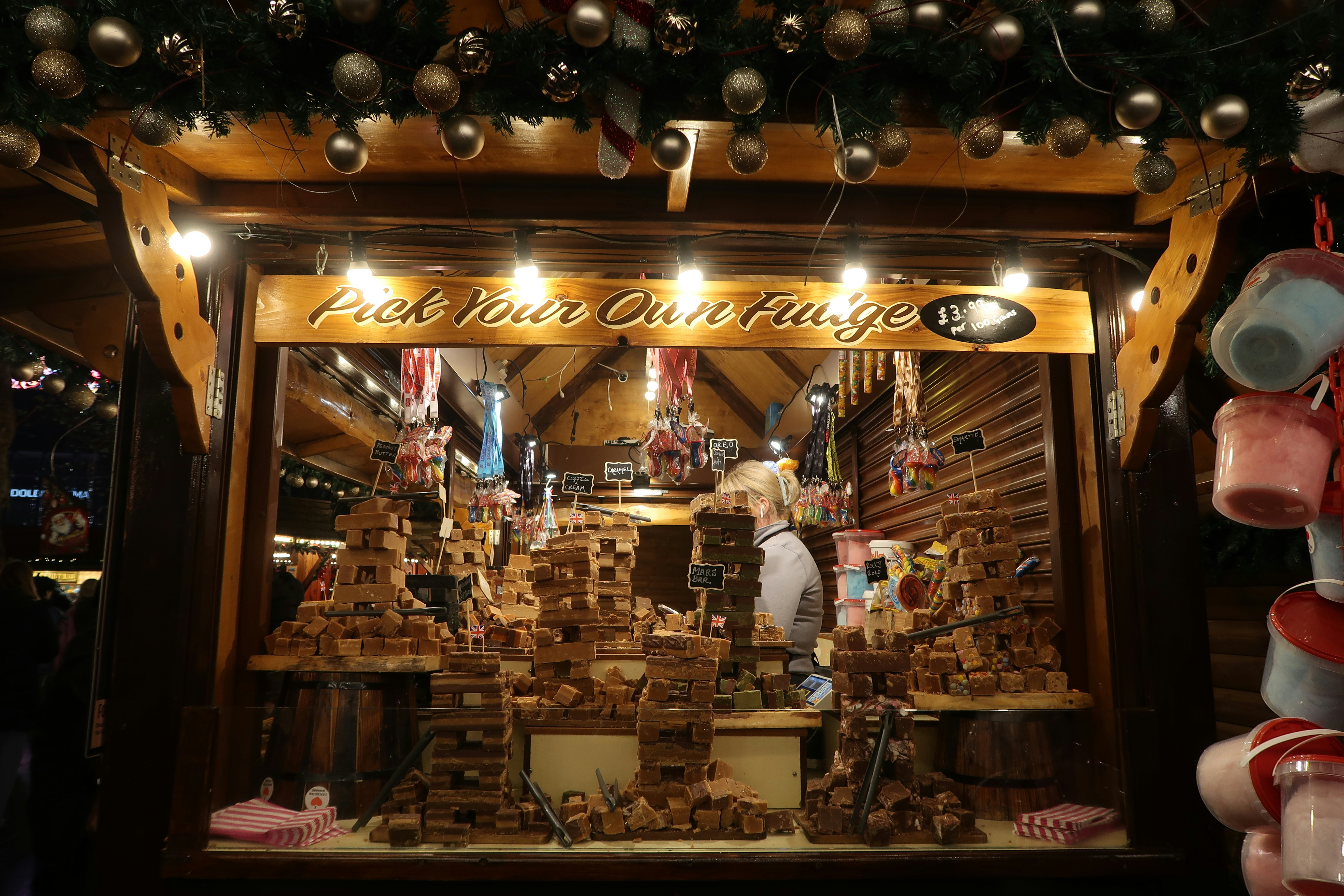A bustling market stall filled with various fudge blocks, inviting customers to choose their favorites. Festive decorations enhance the warm atmosphere.