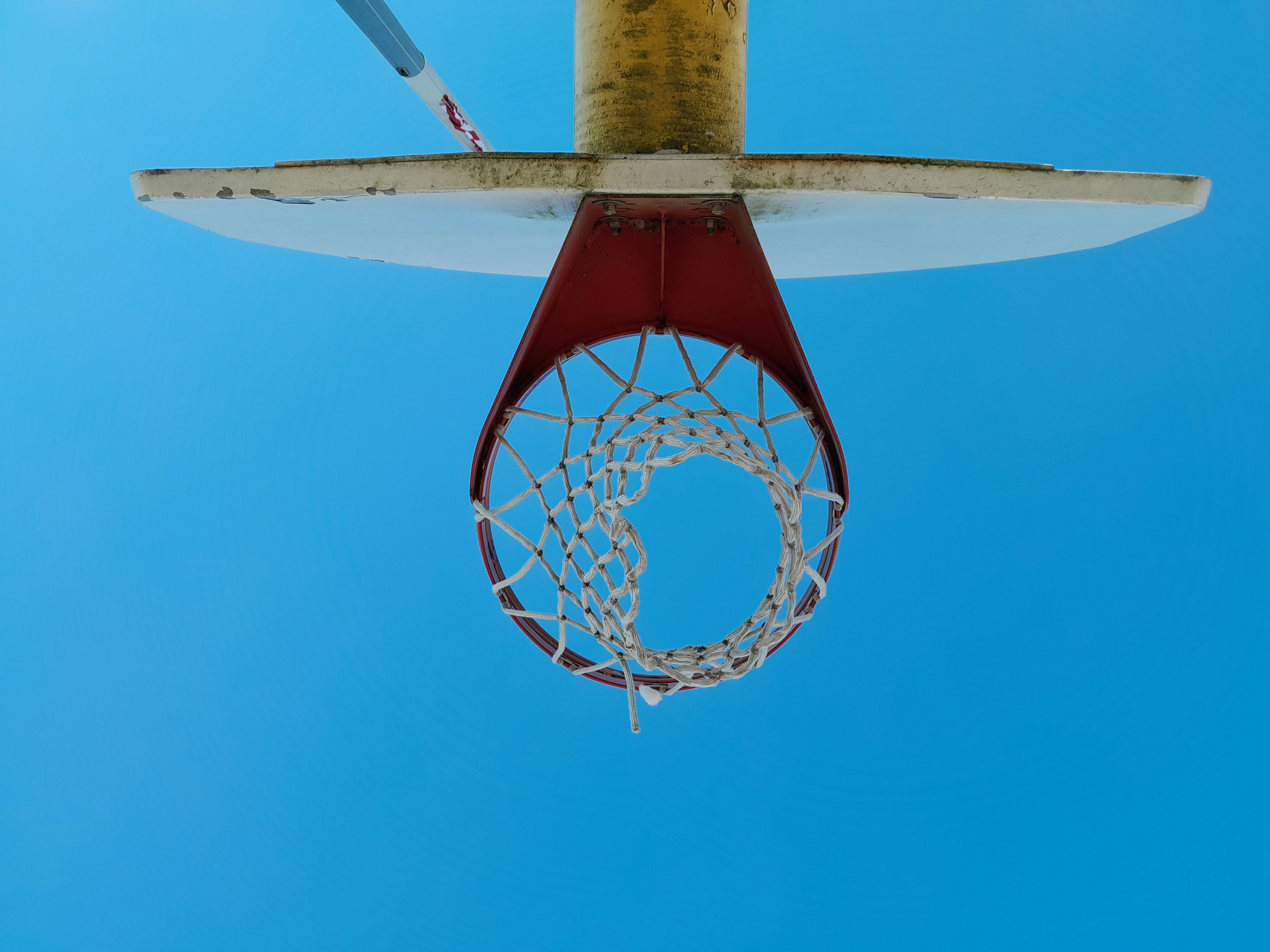 Low-angle photograph of a basketball hoop against a vivid blue sky, highlighting the red rim and white net.