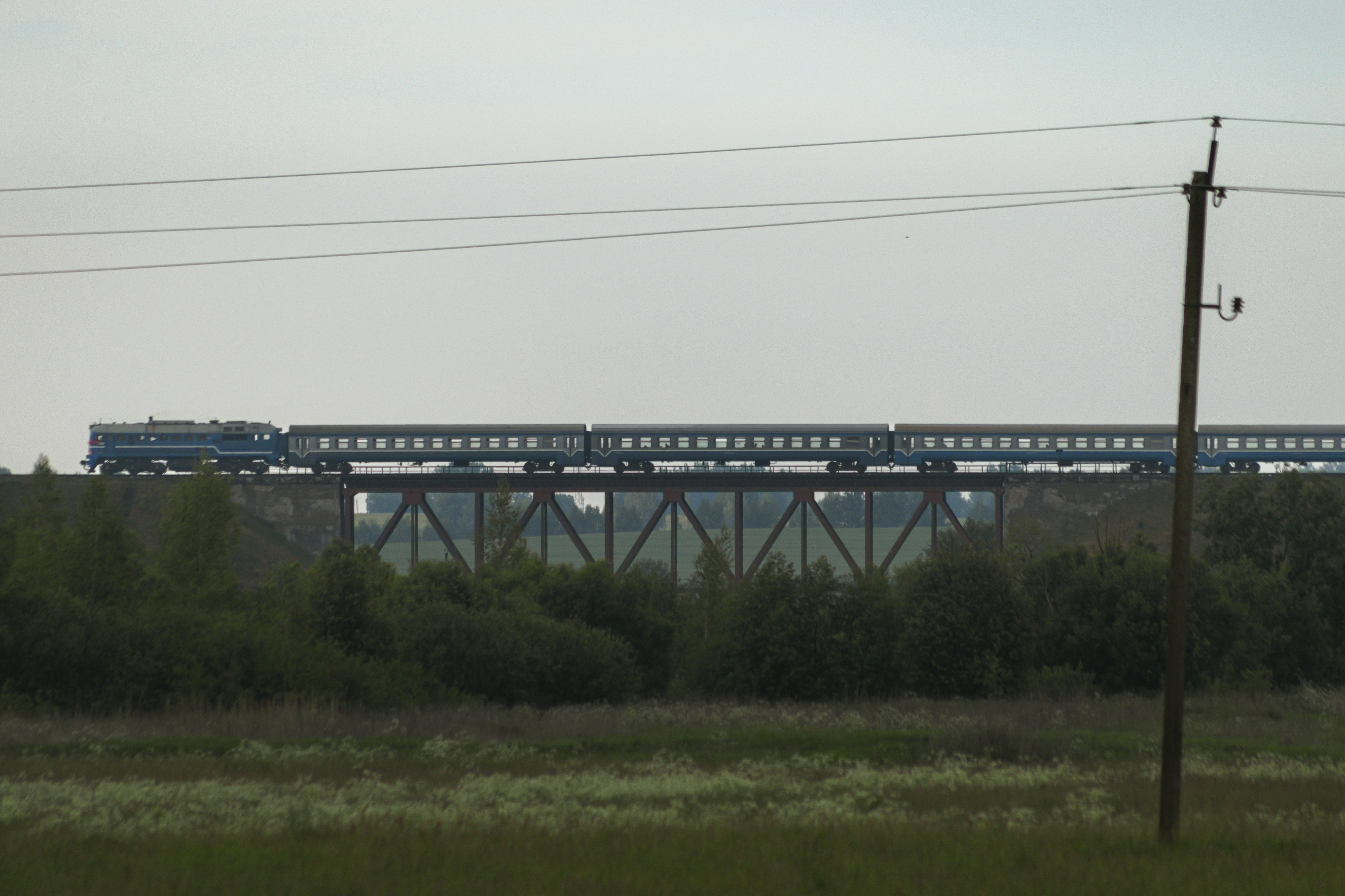 Across the Prairie Viaduct: a blue passenger train threads a steel trellis beneath a gray sky