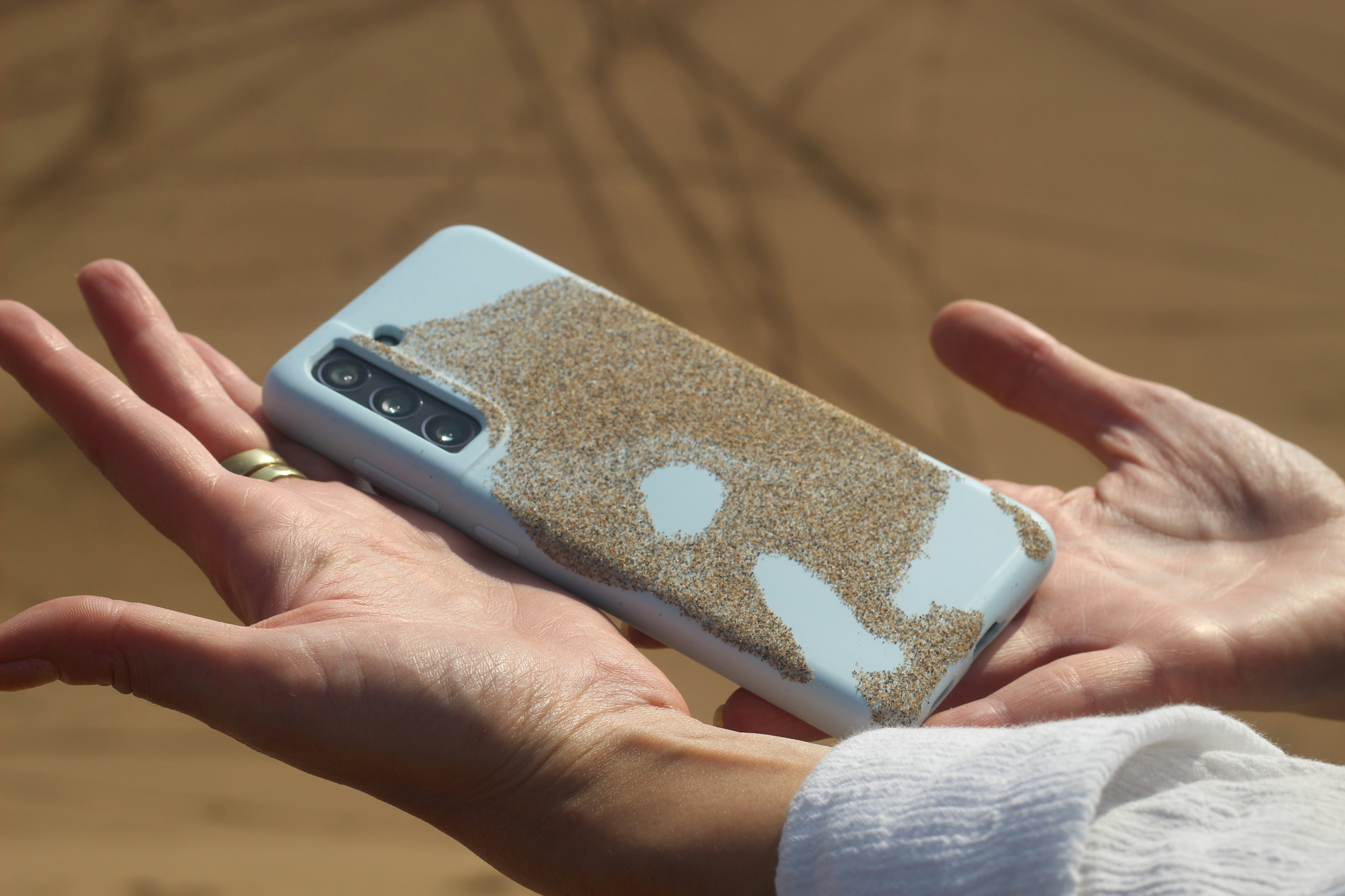 Sand-streaked Blue Phone Case Cradled in Sunlit Hands