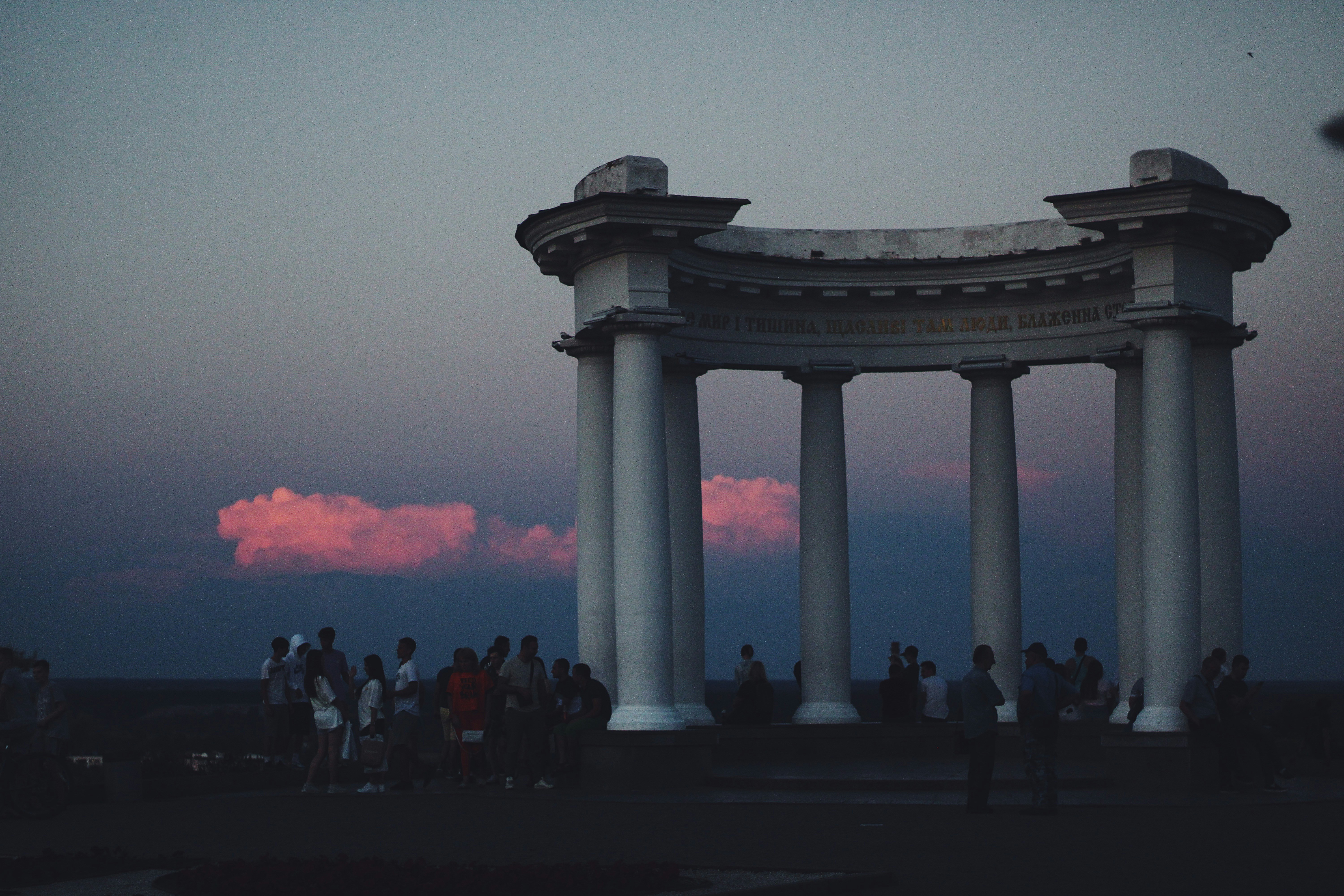 Dusk at the Seaside Colonnade: A Quiet Crowd Beneath the Pink Clouds