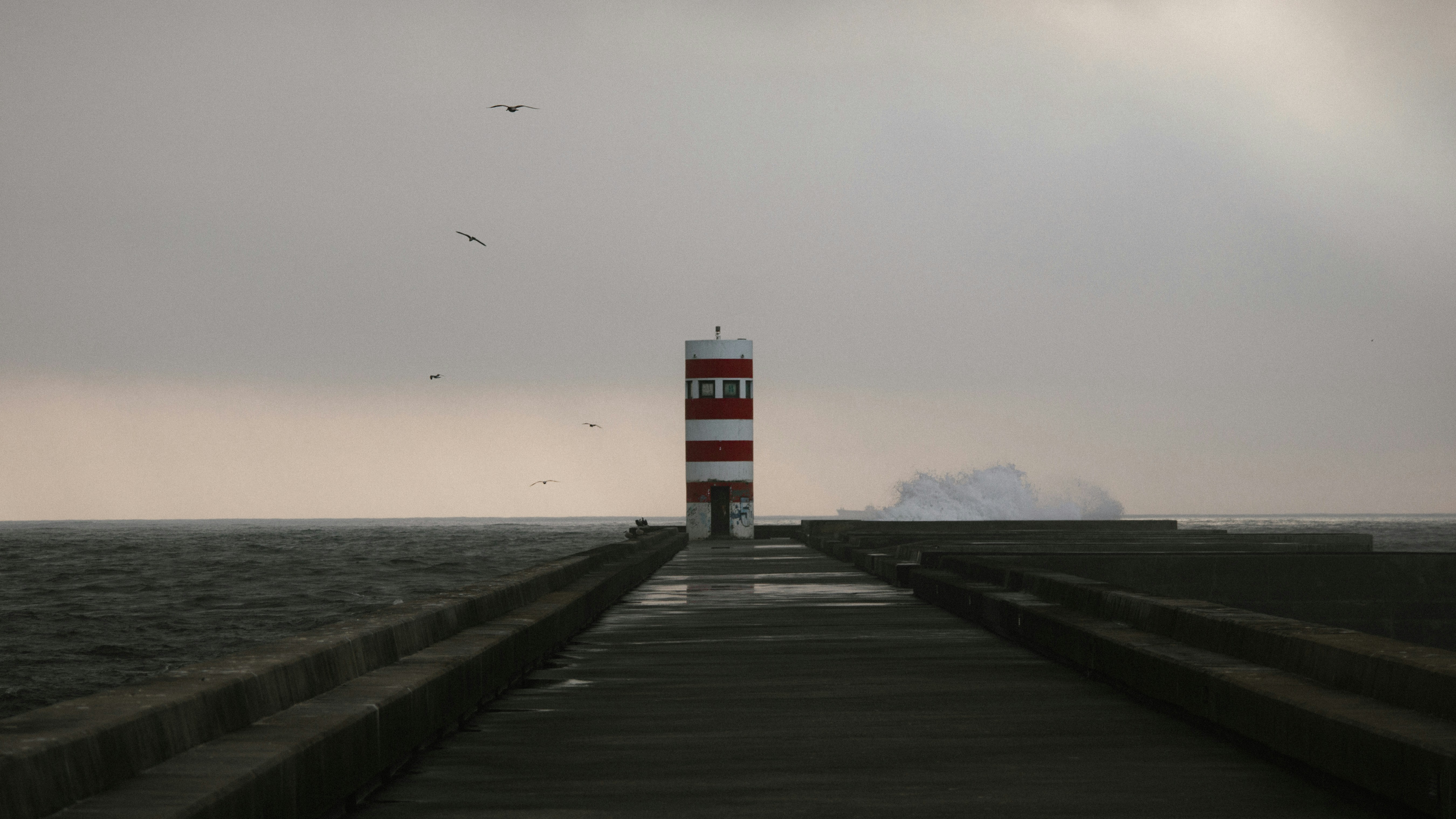 Beacon at the Pier's Vanishing Point: A Striped Lighthouse Against a Moody Horizon