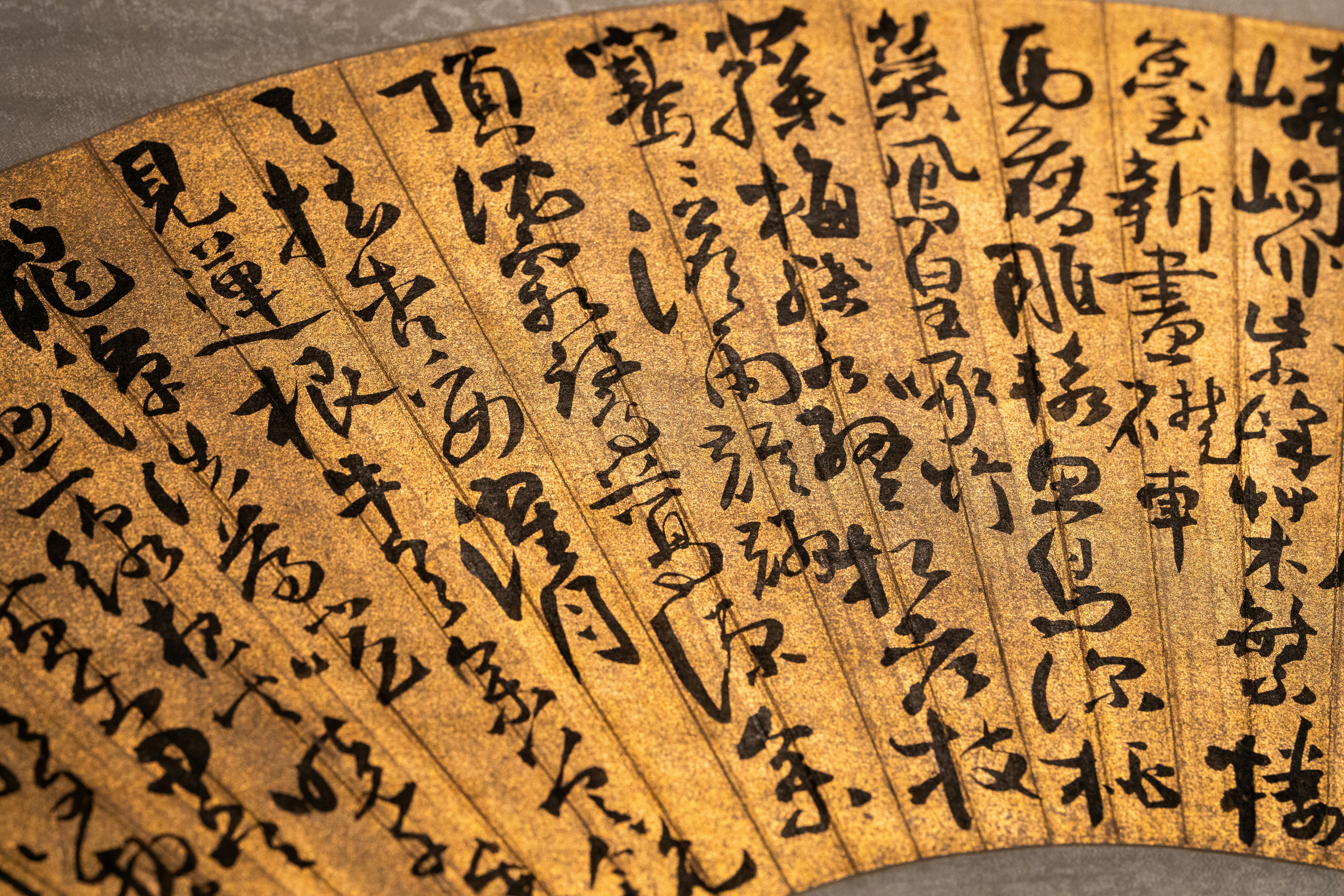 Curved bamboo fan adorned with flowing calligraphy in black ink.
