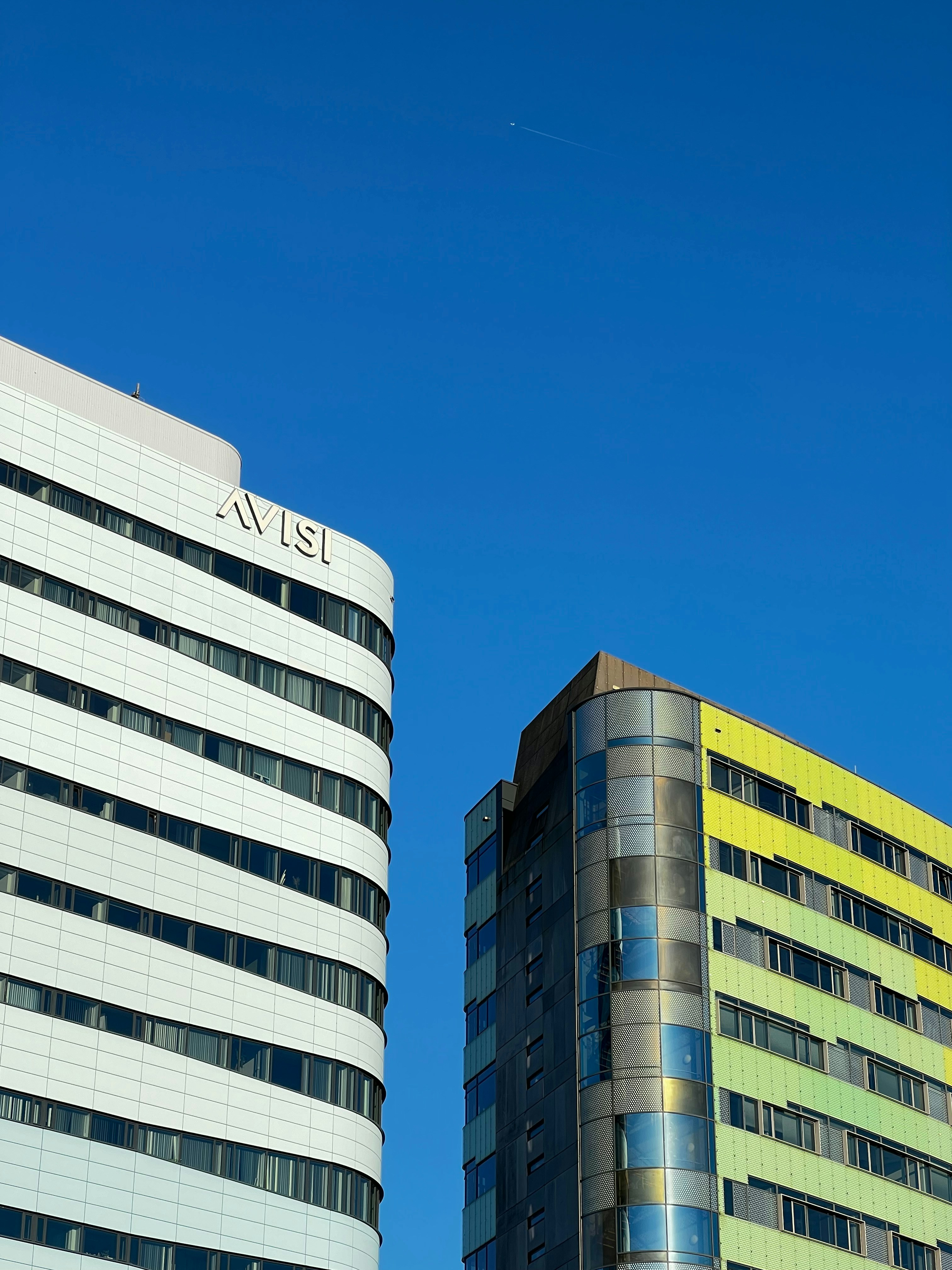 Two modern buildings juxtaposed against a clear blue sky, showcasing distinct architectural styles and materials.