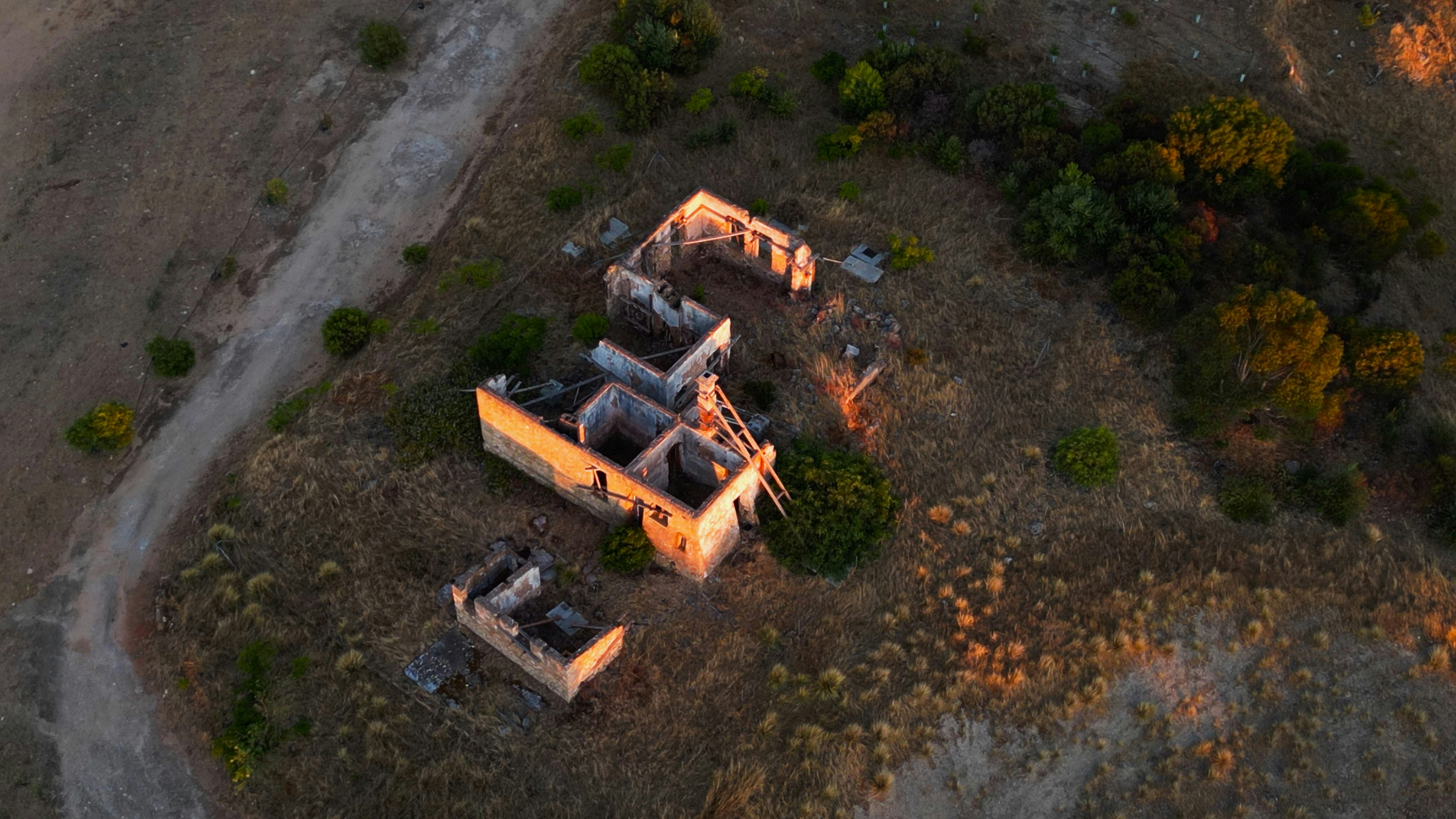Abandoned stone structure surrounded by overgrown vegetation in a desolate landscape at sunset.