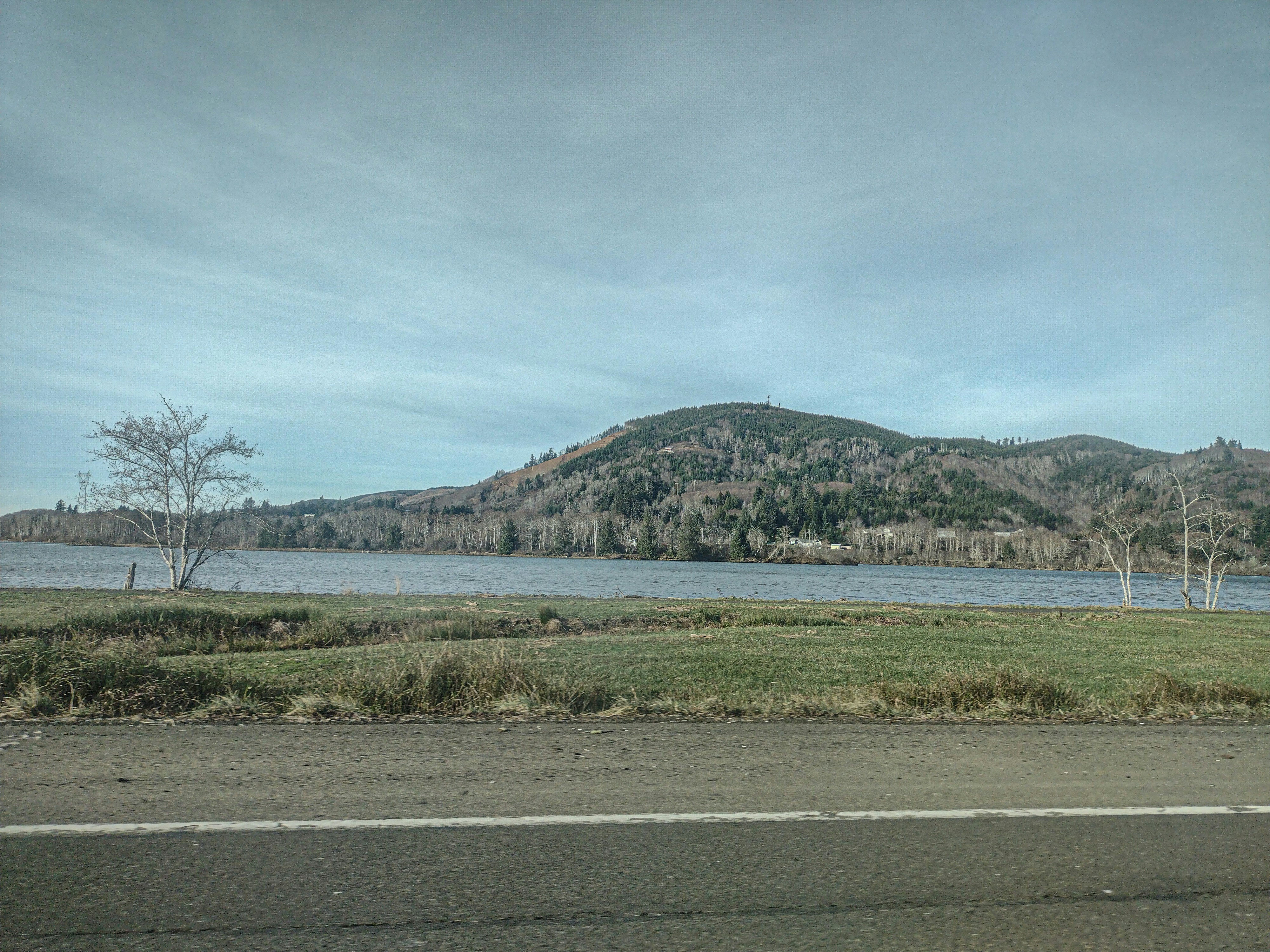 Calm lake bordered by a green field and distant hills under a cloudy sky.